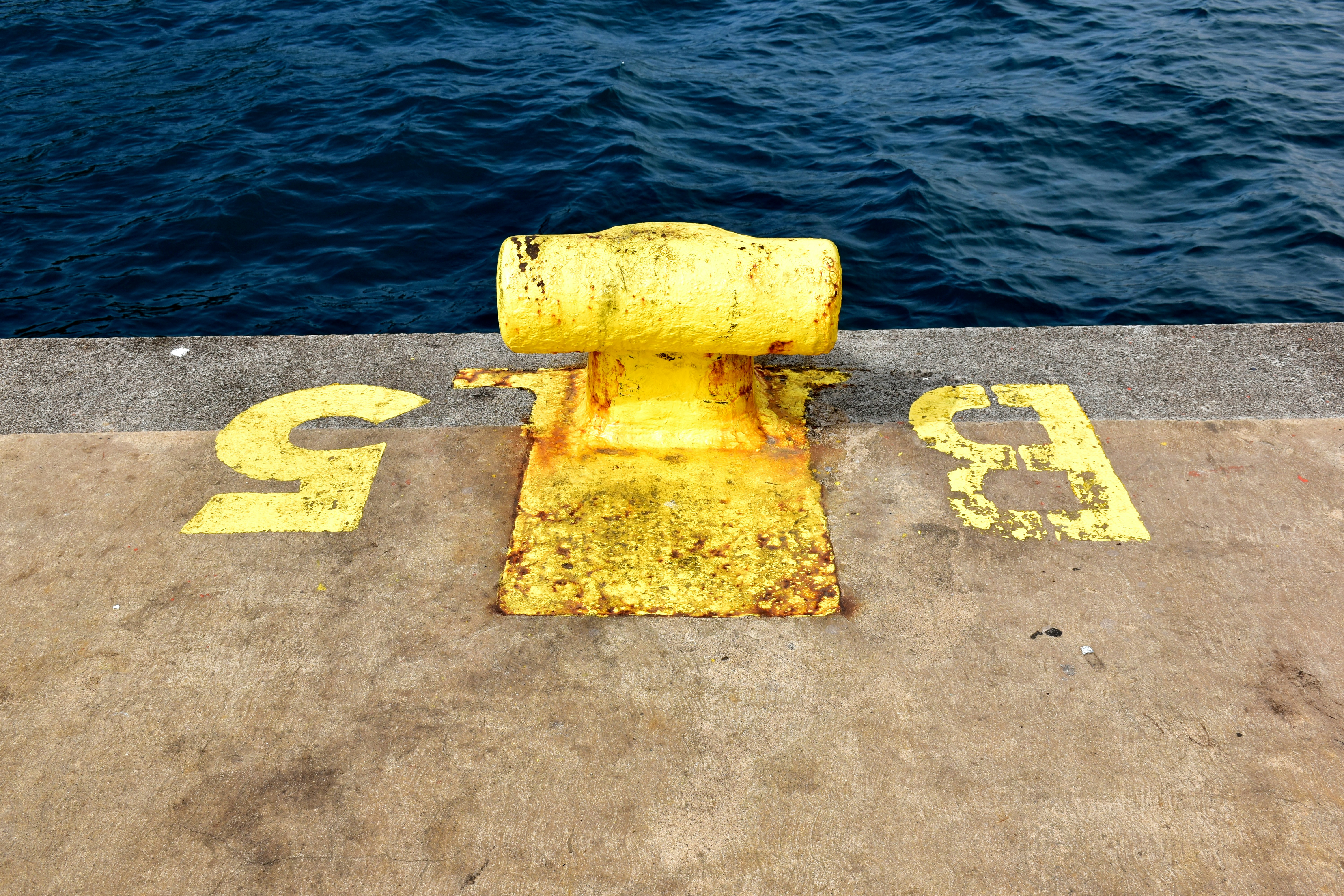 Sun-bleached Yellow Bollard at the Dock's Edge Framing the Deep Blue Sea