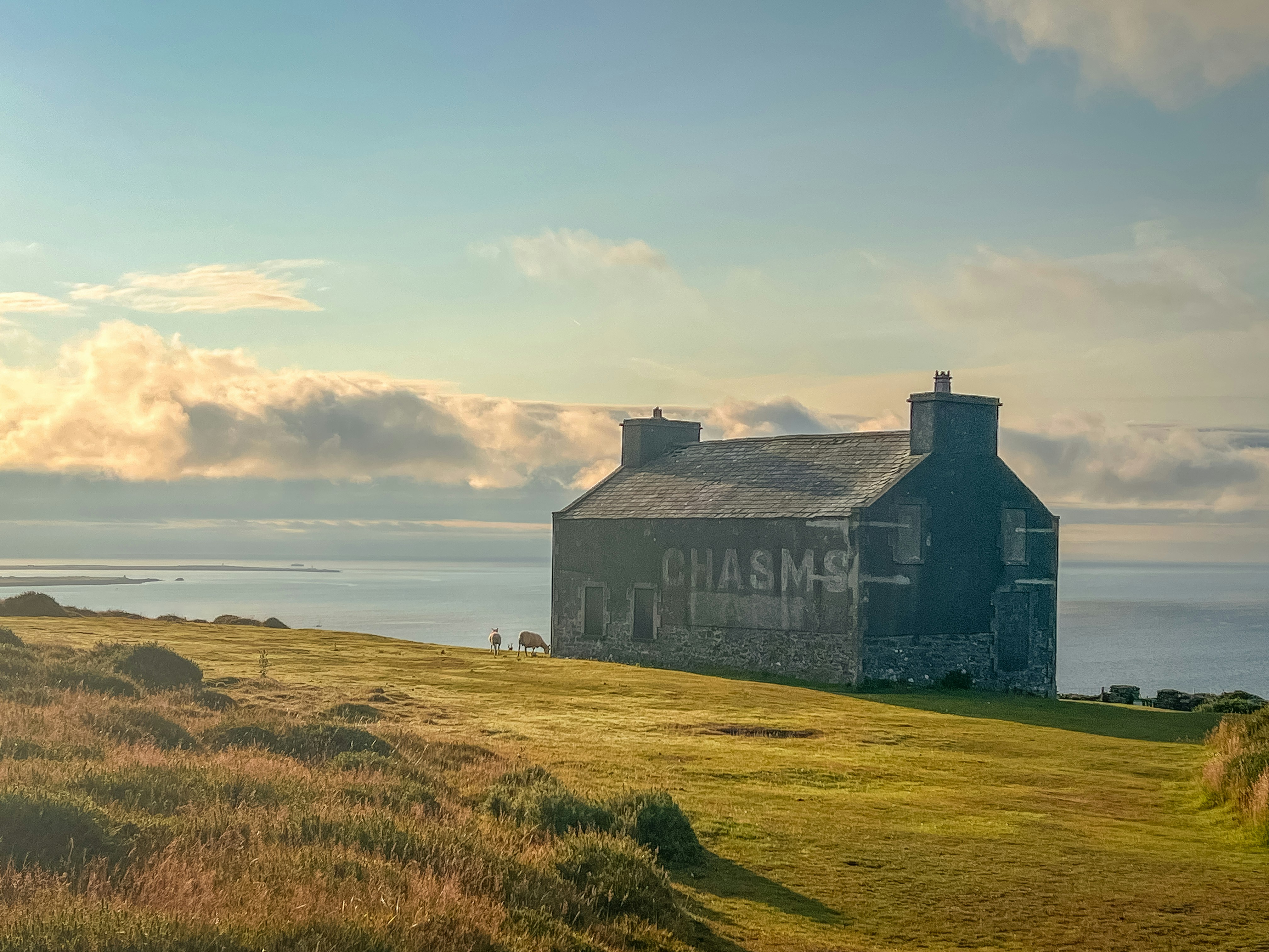 Stone building perched on a lush hillside overlooking a calm sea under a vibrant sky.
