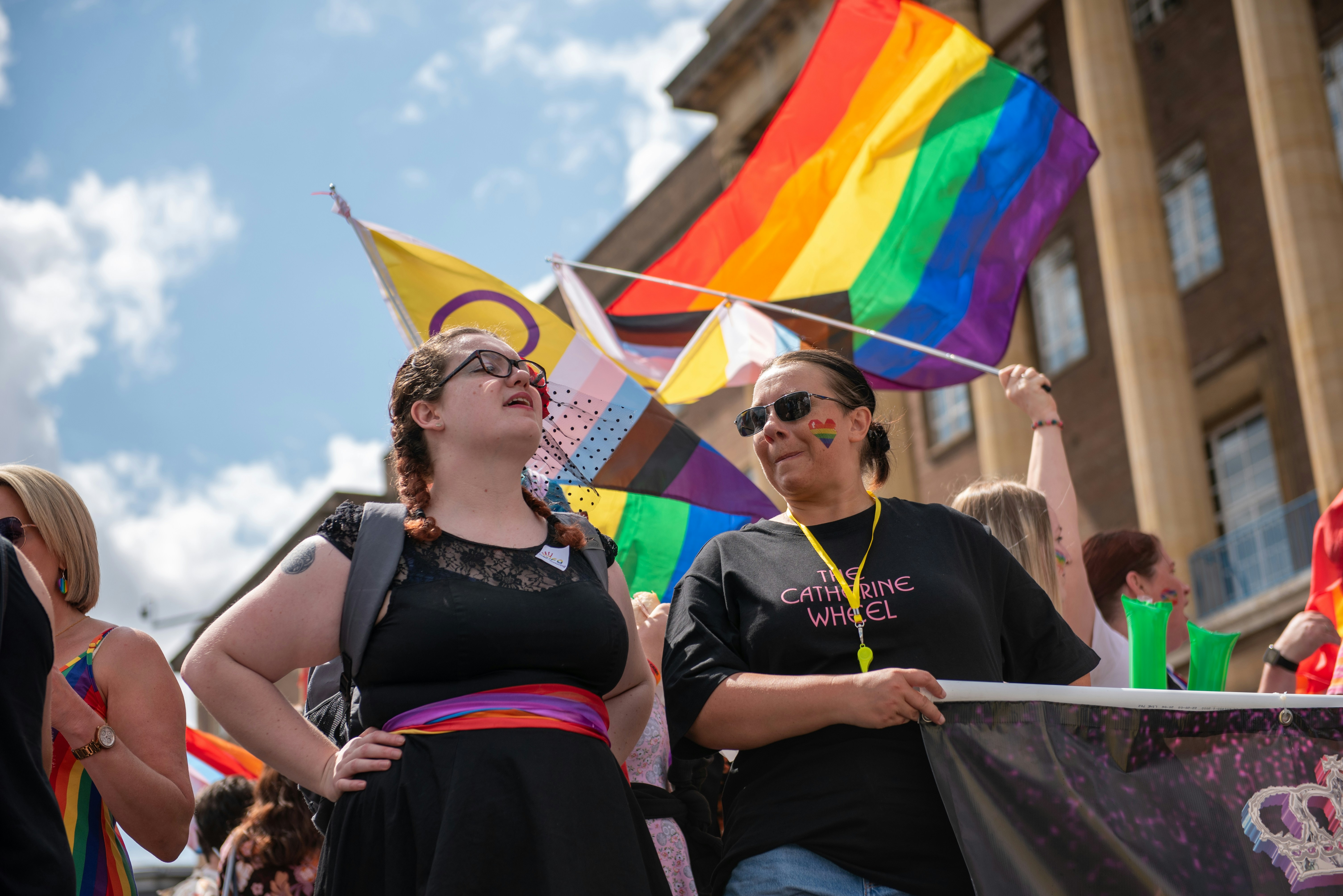 Two Pride Parade Participants Stand Confidently Under Rainbow Flags in an Urban Street