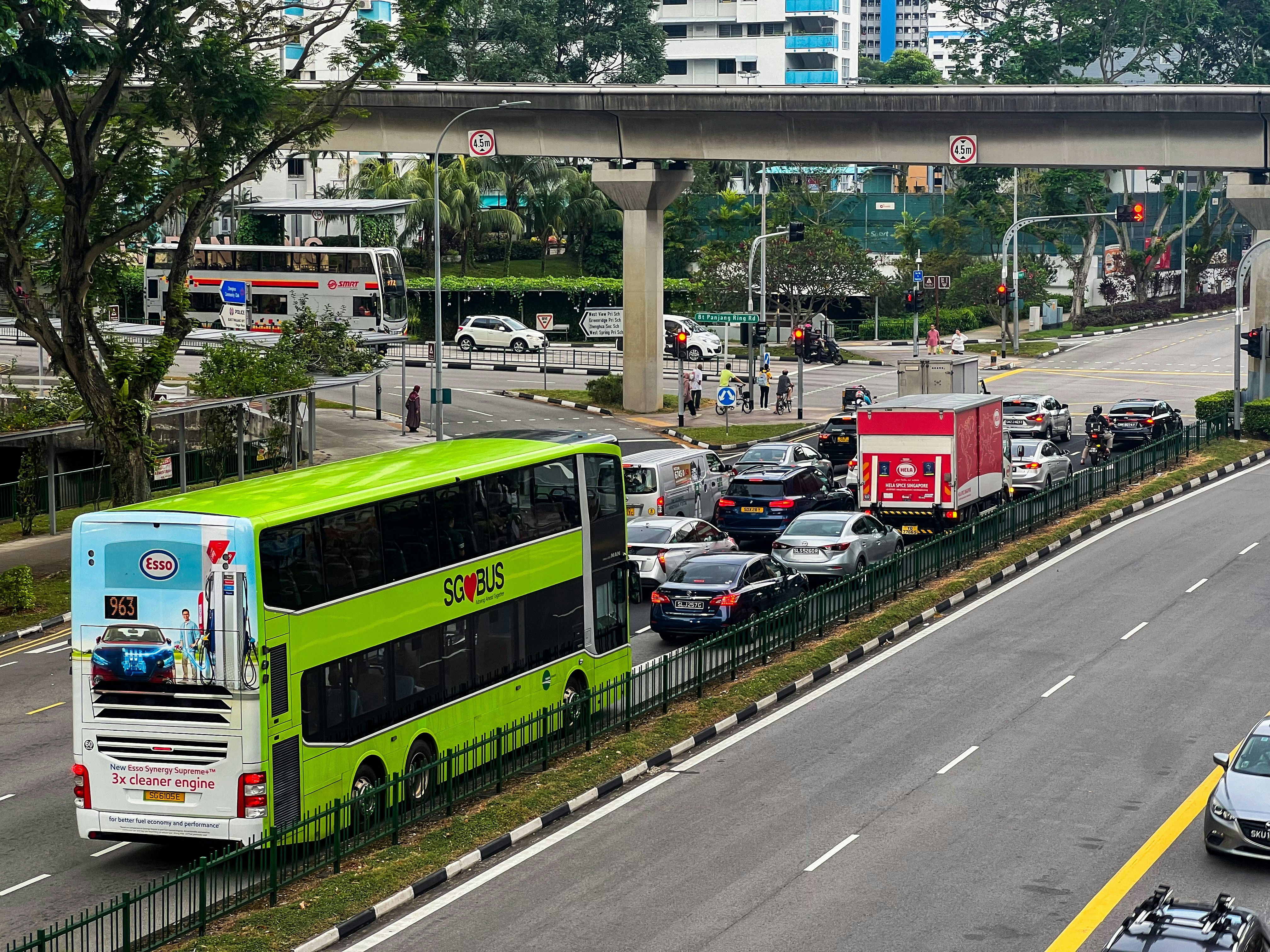 Double-decker bus and vehicles navigating a busy urban roadway beneath elevated tracks.