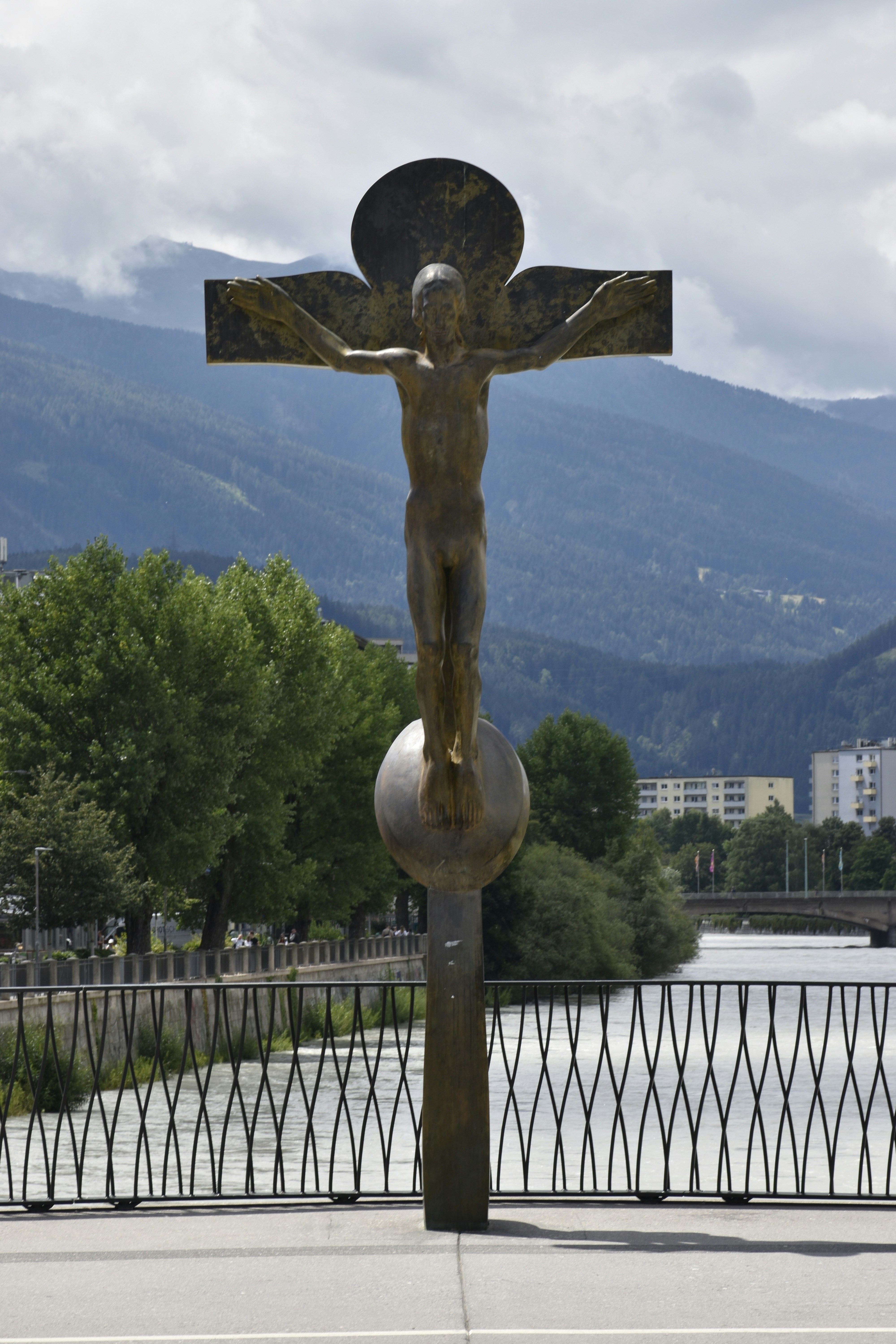 Bronze Crucifix Over the River: A Silent Alpine Promenade Statue Framed by Mountains