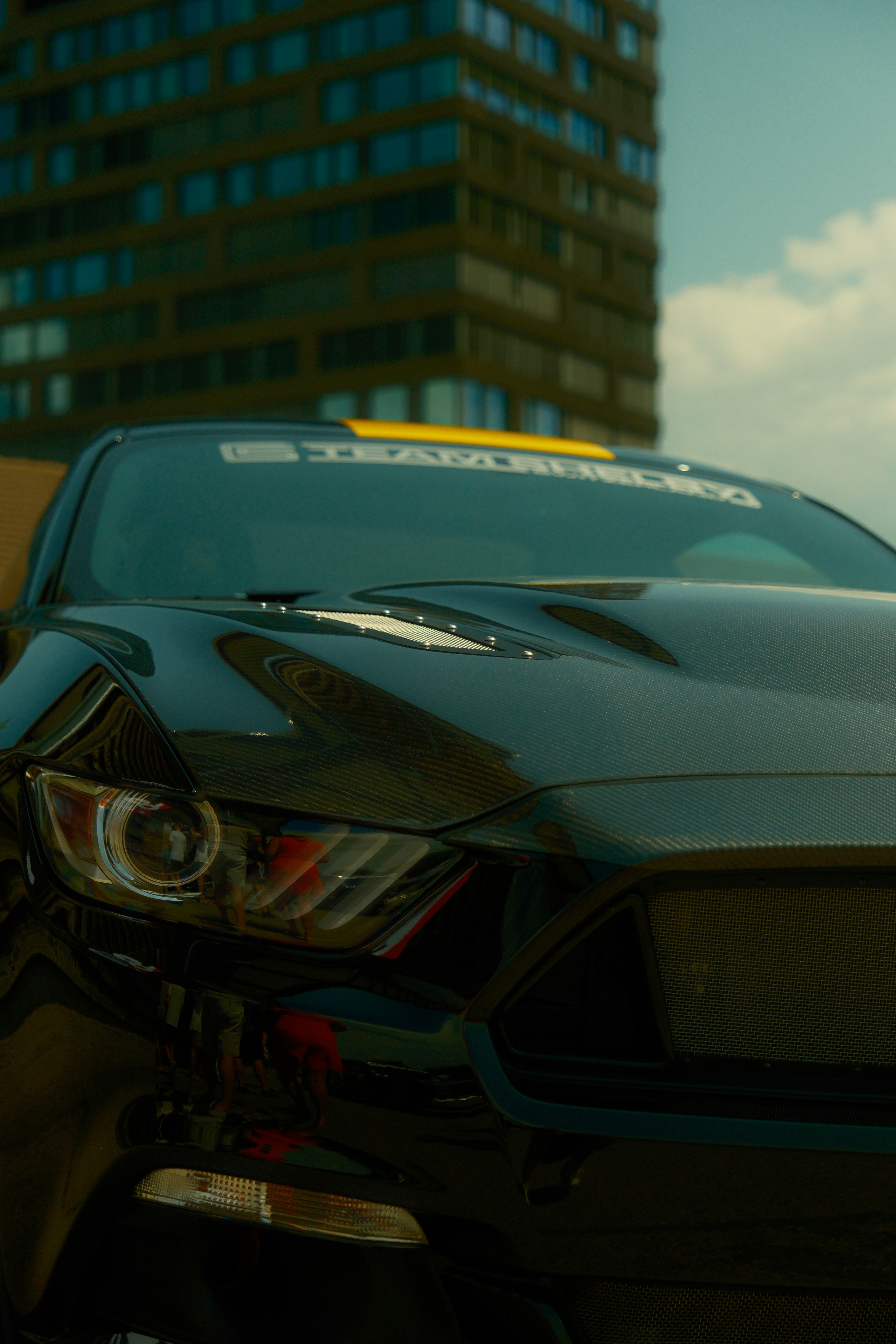 Close-up of a black Mustang showcasing its aggressive design and sleek lines against an urban backdrop.