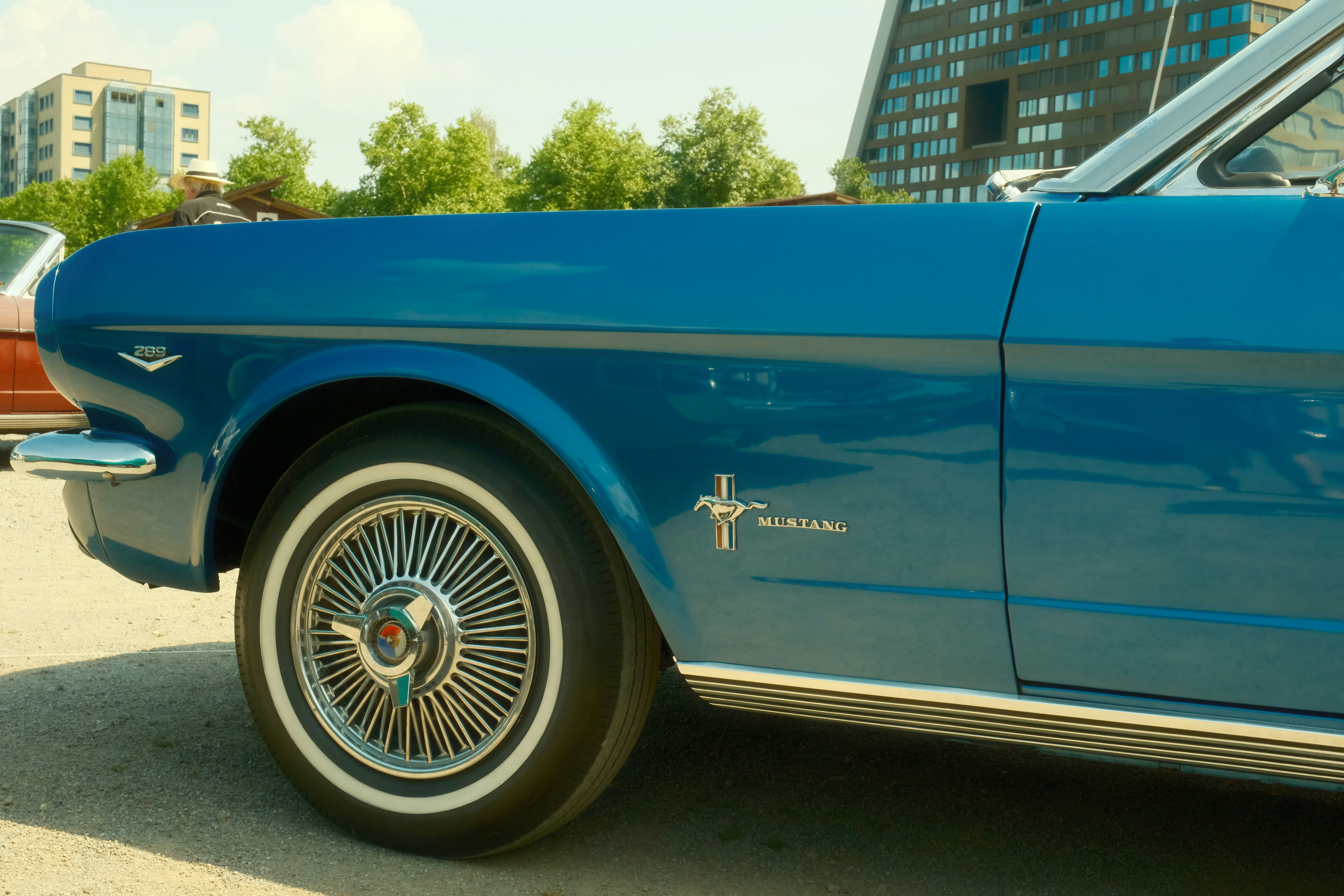 Sunlit Blue Mustang: chrome wheel detail and side emblem against an urban backdrop