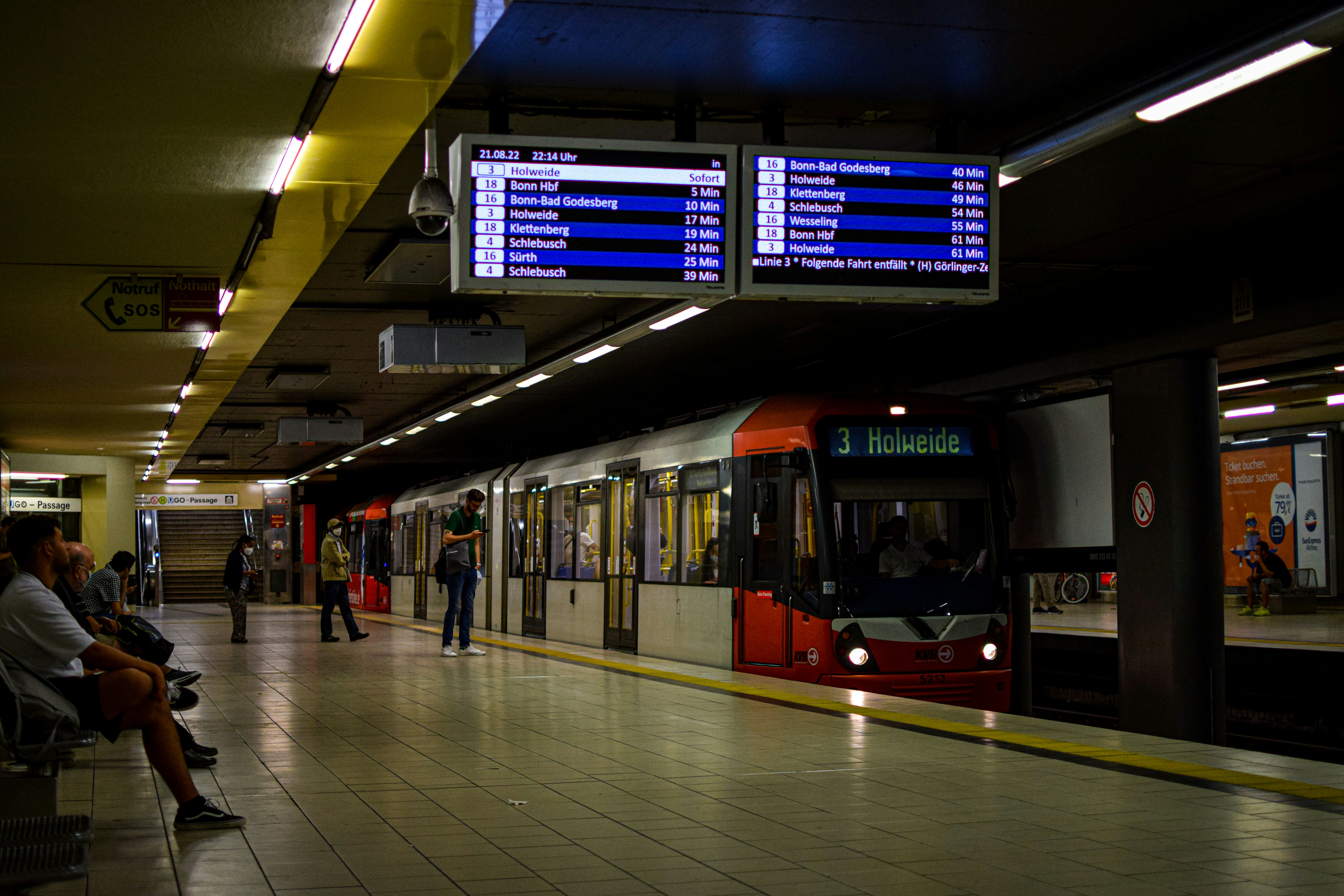 Subway train arriving at a dimly lit underground station with digital schedules overhead.