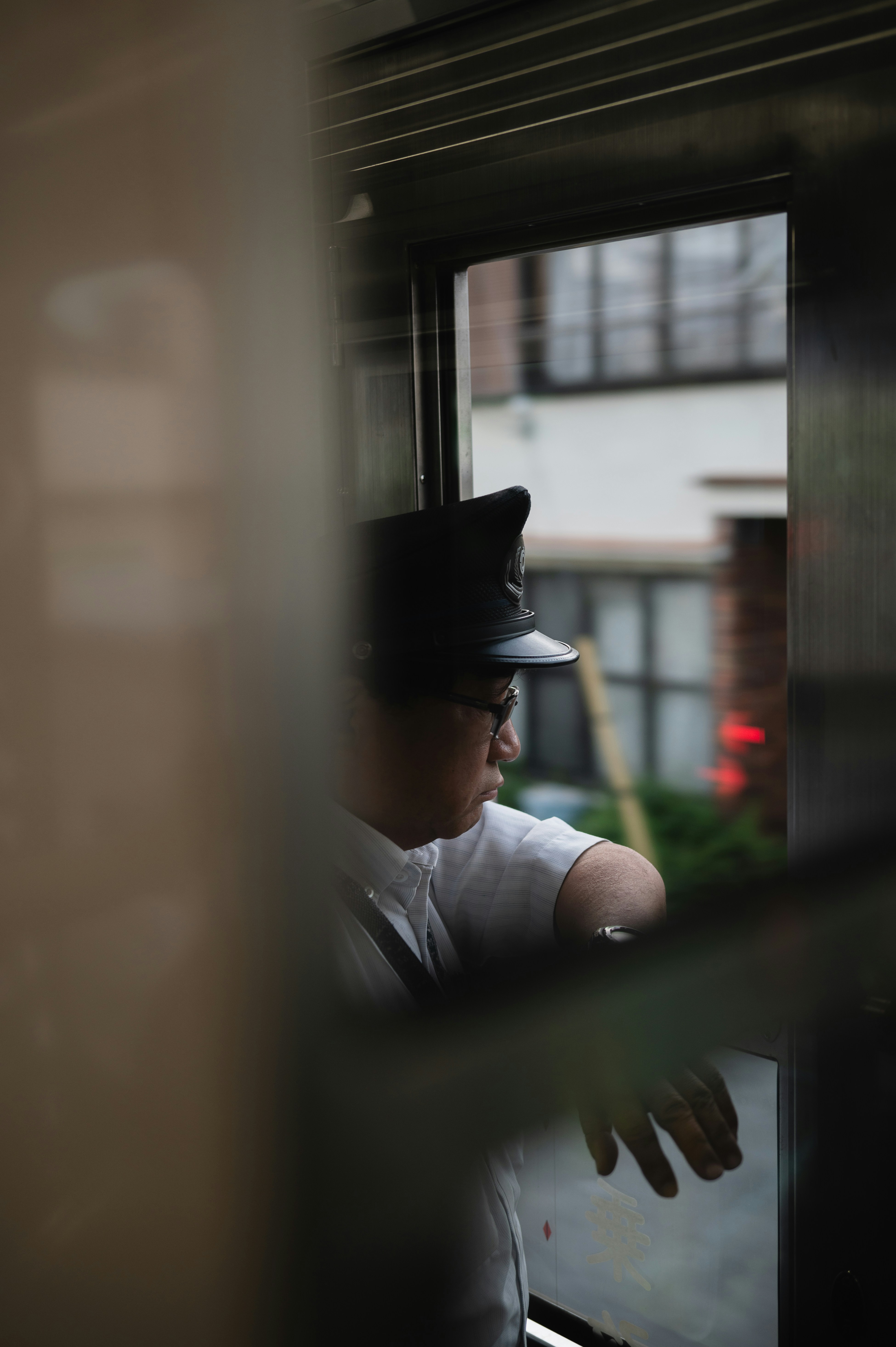 A train conductor gazes thoughtfully from the doorway, framed by the soft blur of the carriage interior. The scene captures a moment of quiet vigilance.