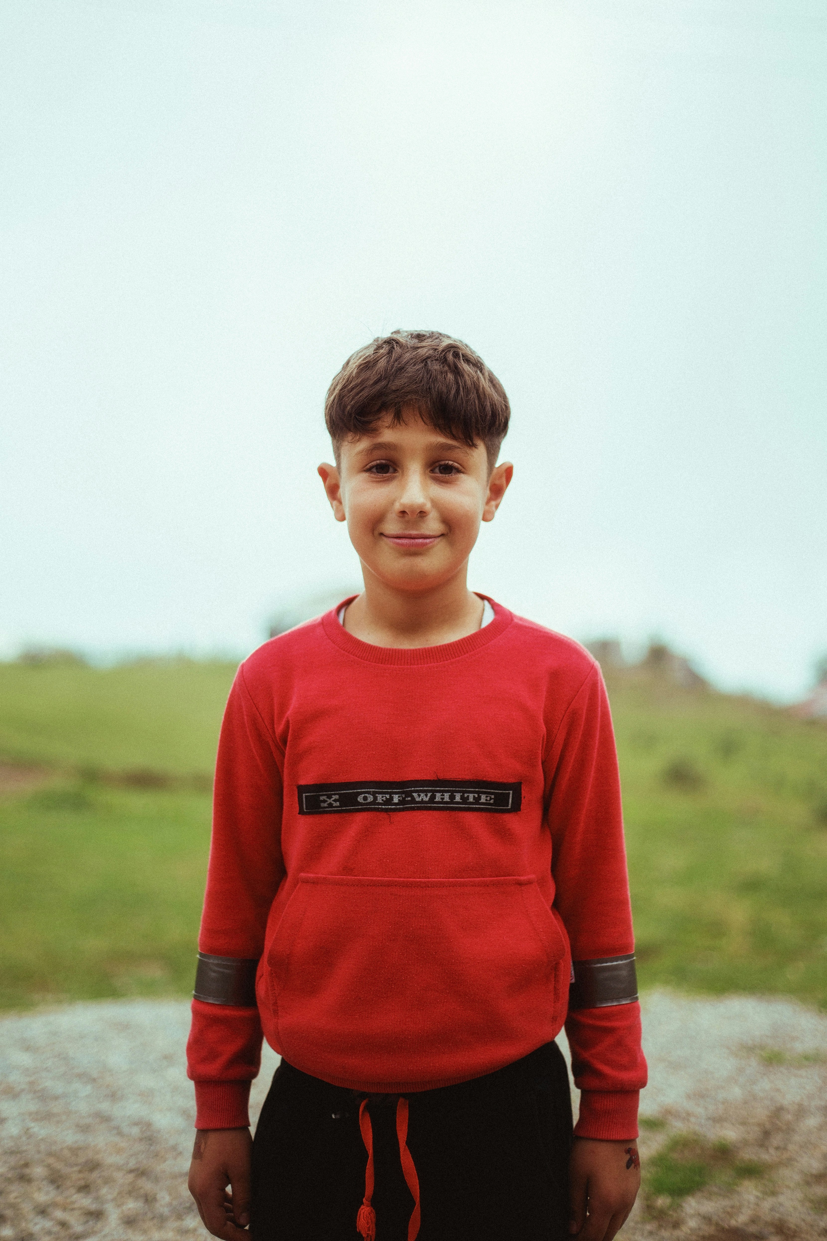 Red sweatshirt, green field: a quiet portrait of a boy in an open day