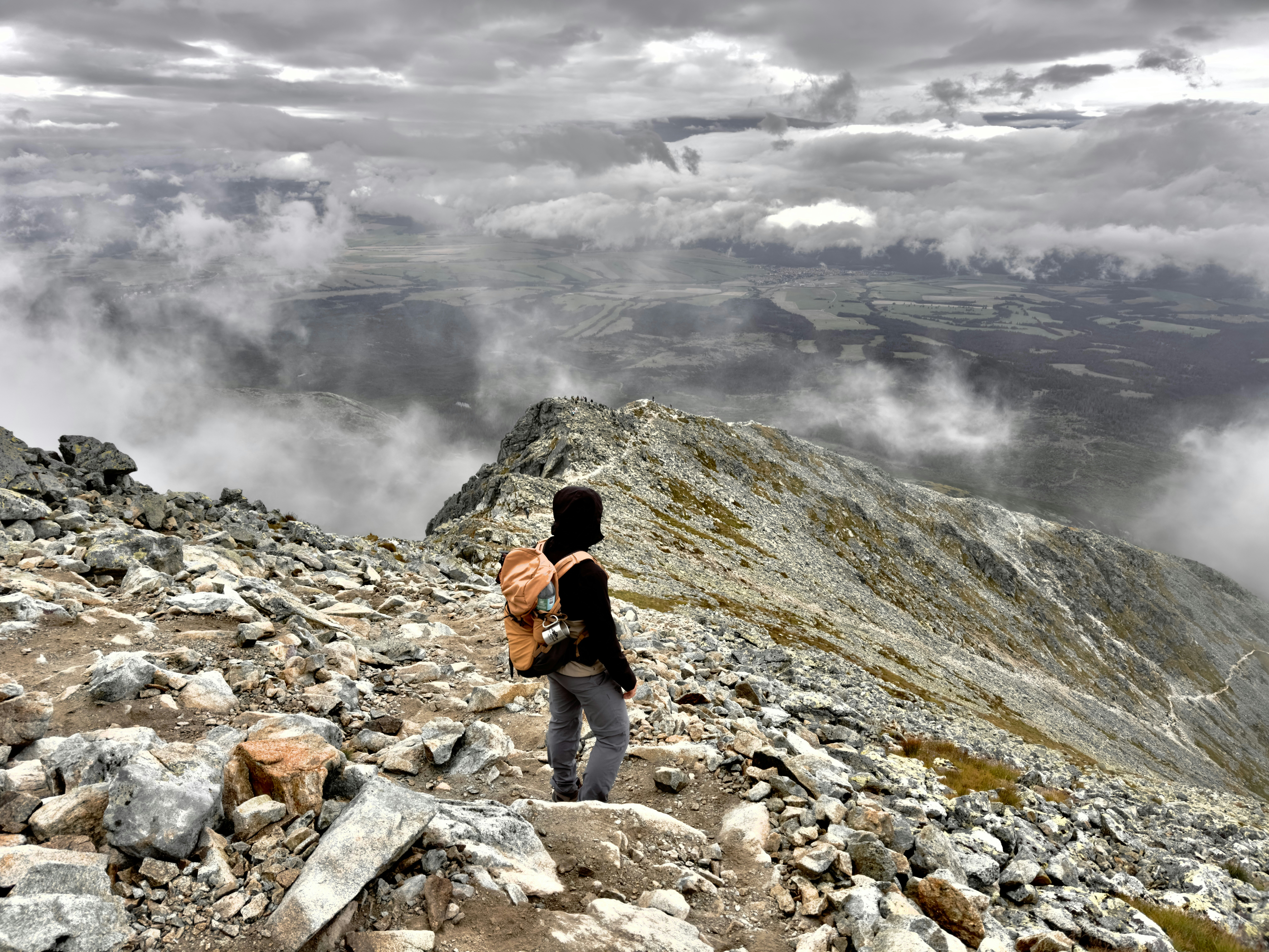 Hiker standing on a rocky mountain ridge enveloped by clouds and mist.