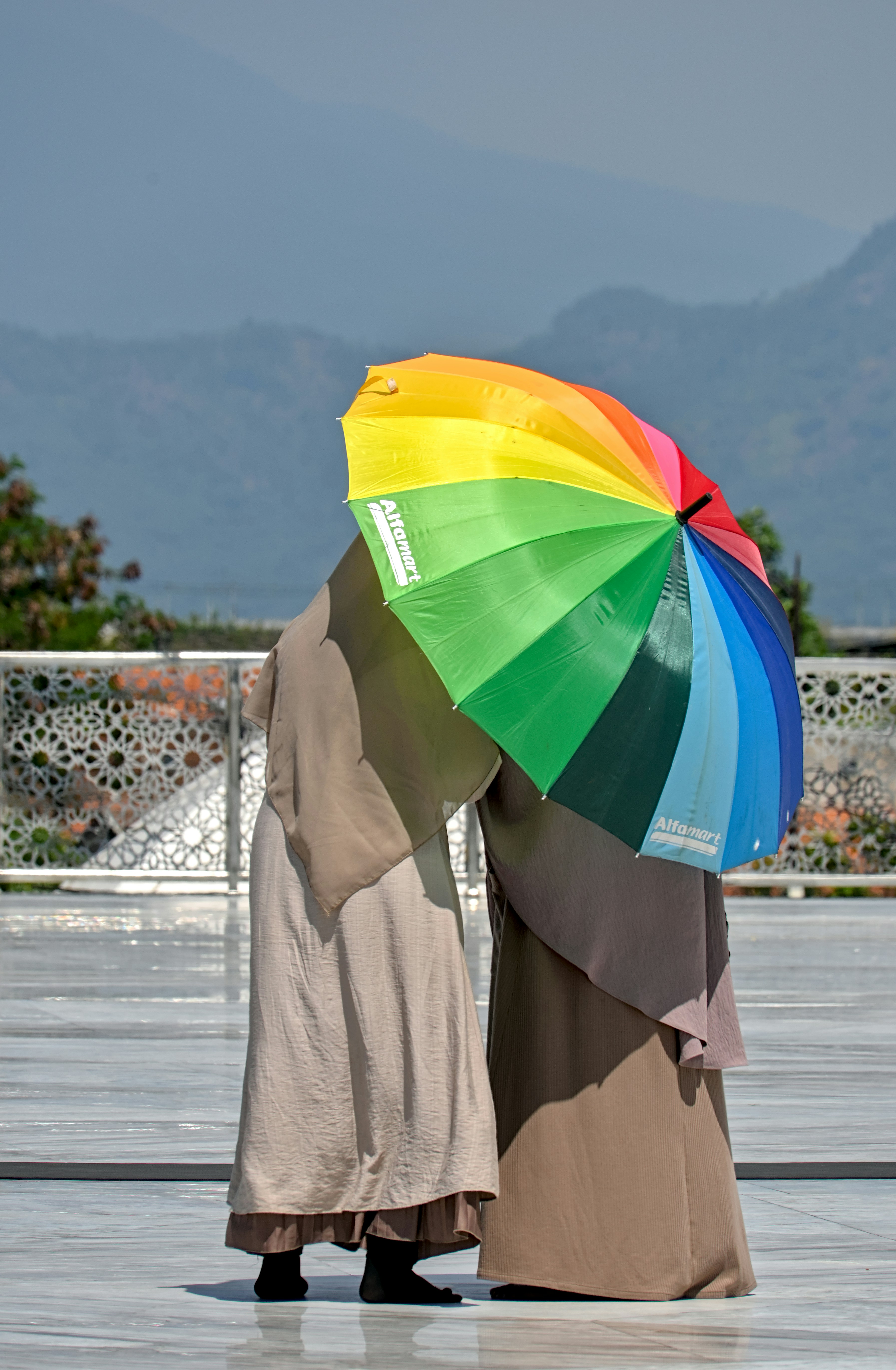 Chromatic Shelter: Rainbow Umbrella Framing Quiet Figures on a Marble Terrace