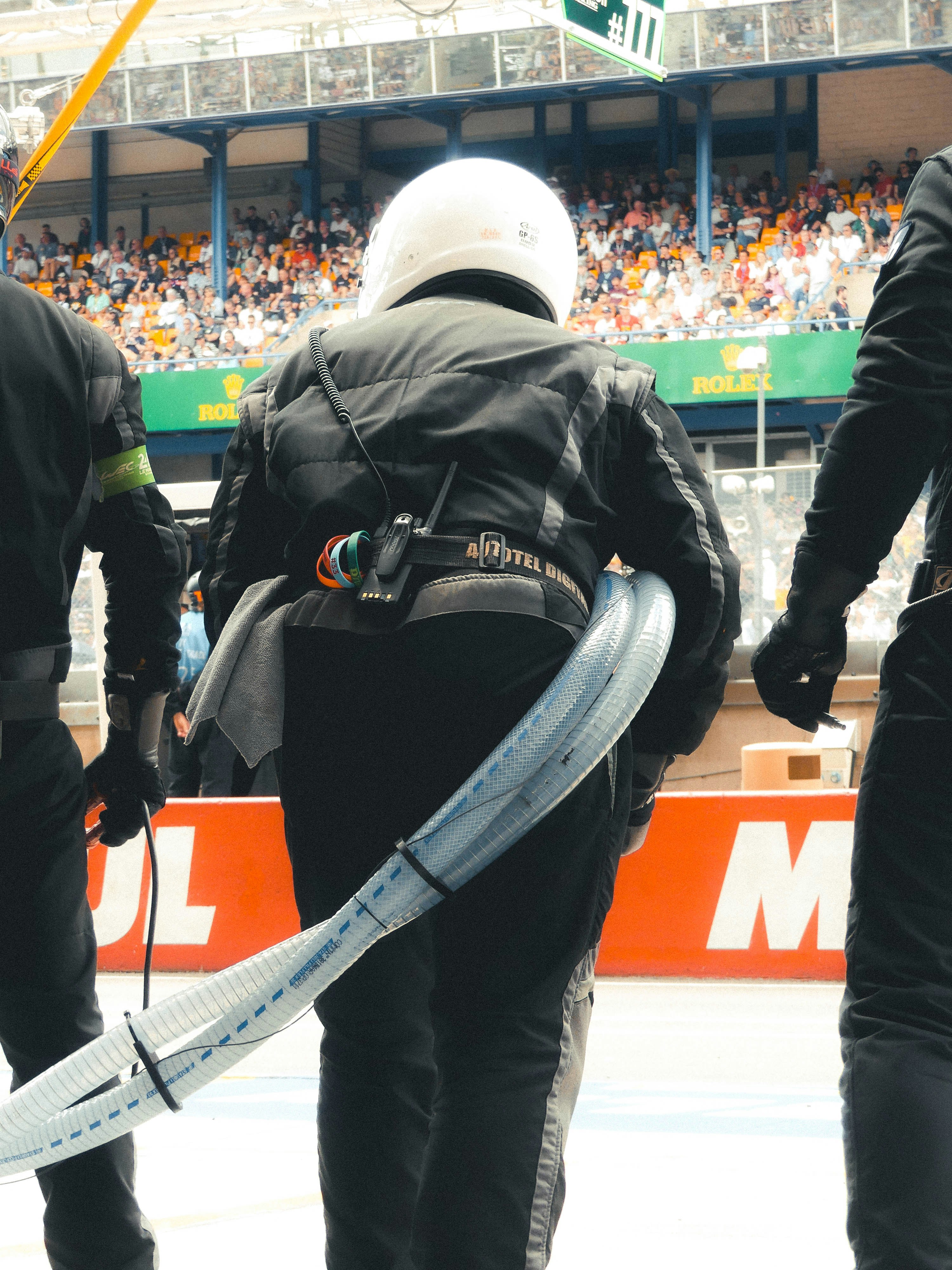 Back of a White-Helmet Technician: Coiled Hose Draped Across the Ice as a Packed Crowd Looks On