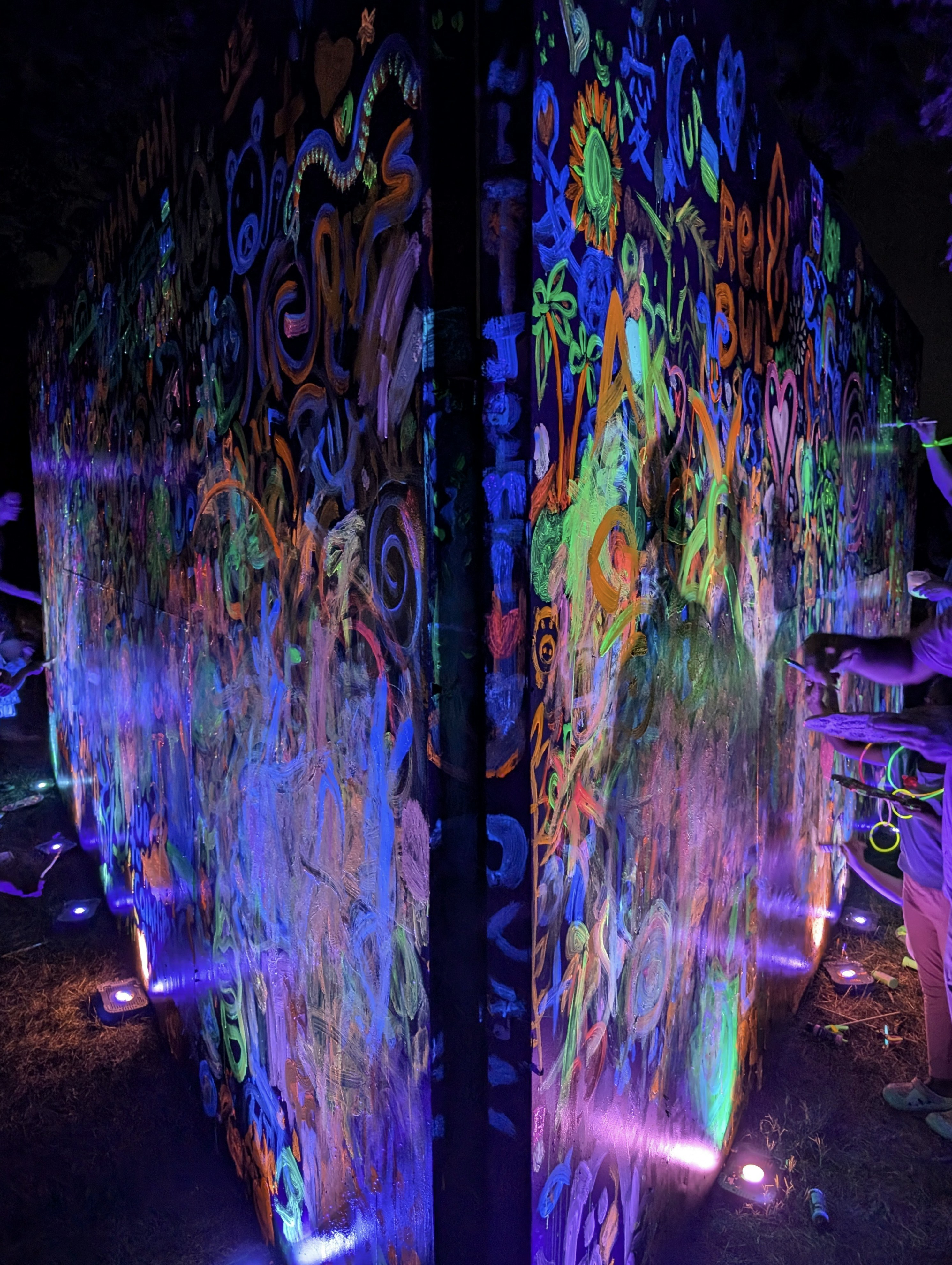 Photograph of a neon graffiti tunnel formed by mirrored panels, with fog and vibrant light reflections.