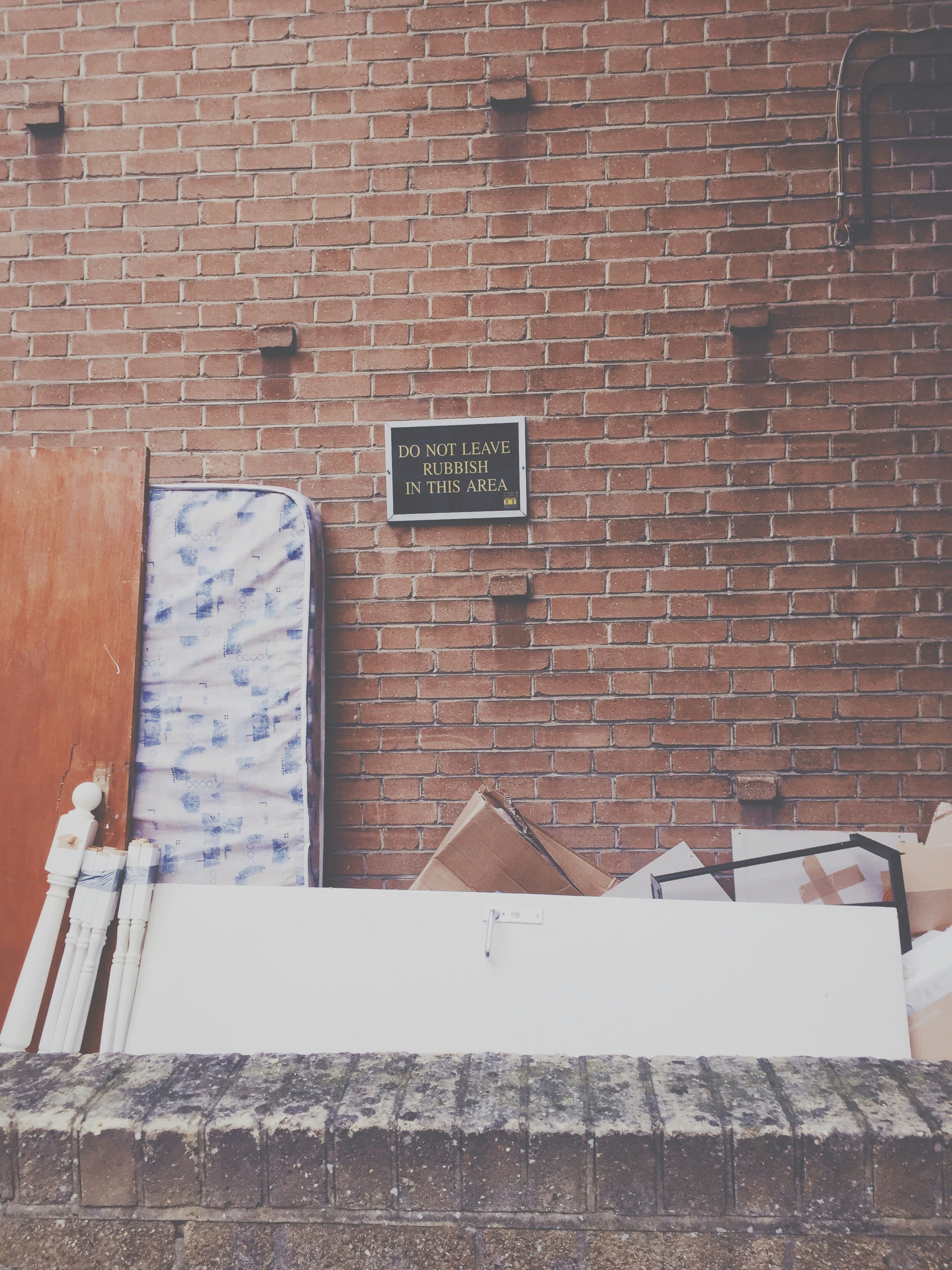 Sign warning against leaving rubbish in a cluttered urban space, surrounded by discarded furniture and materials.