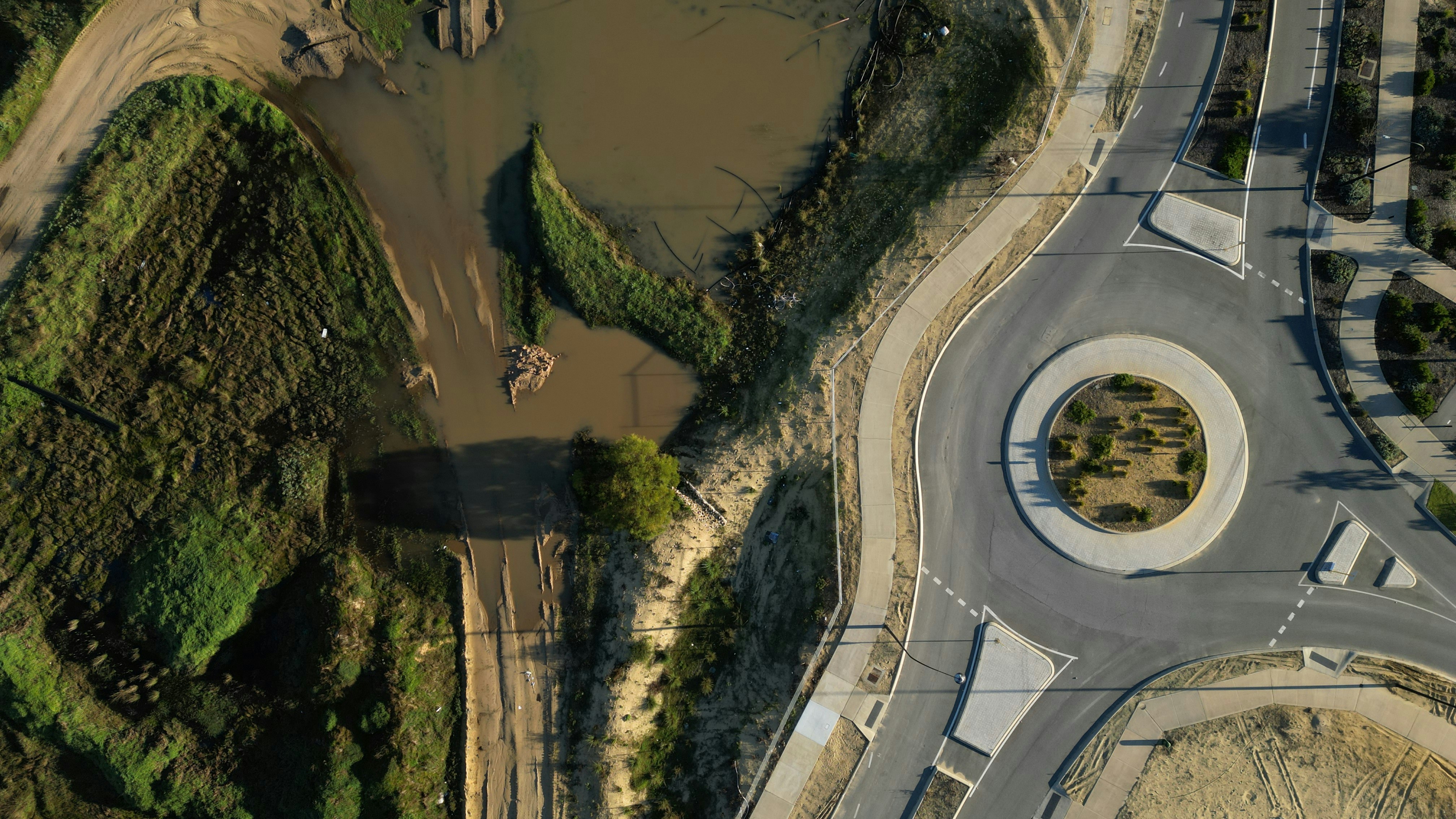 Aerial view of a roundabout surrounded by lush greenery and water, showcasing the blend of nature and urban planning.