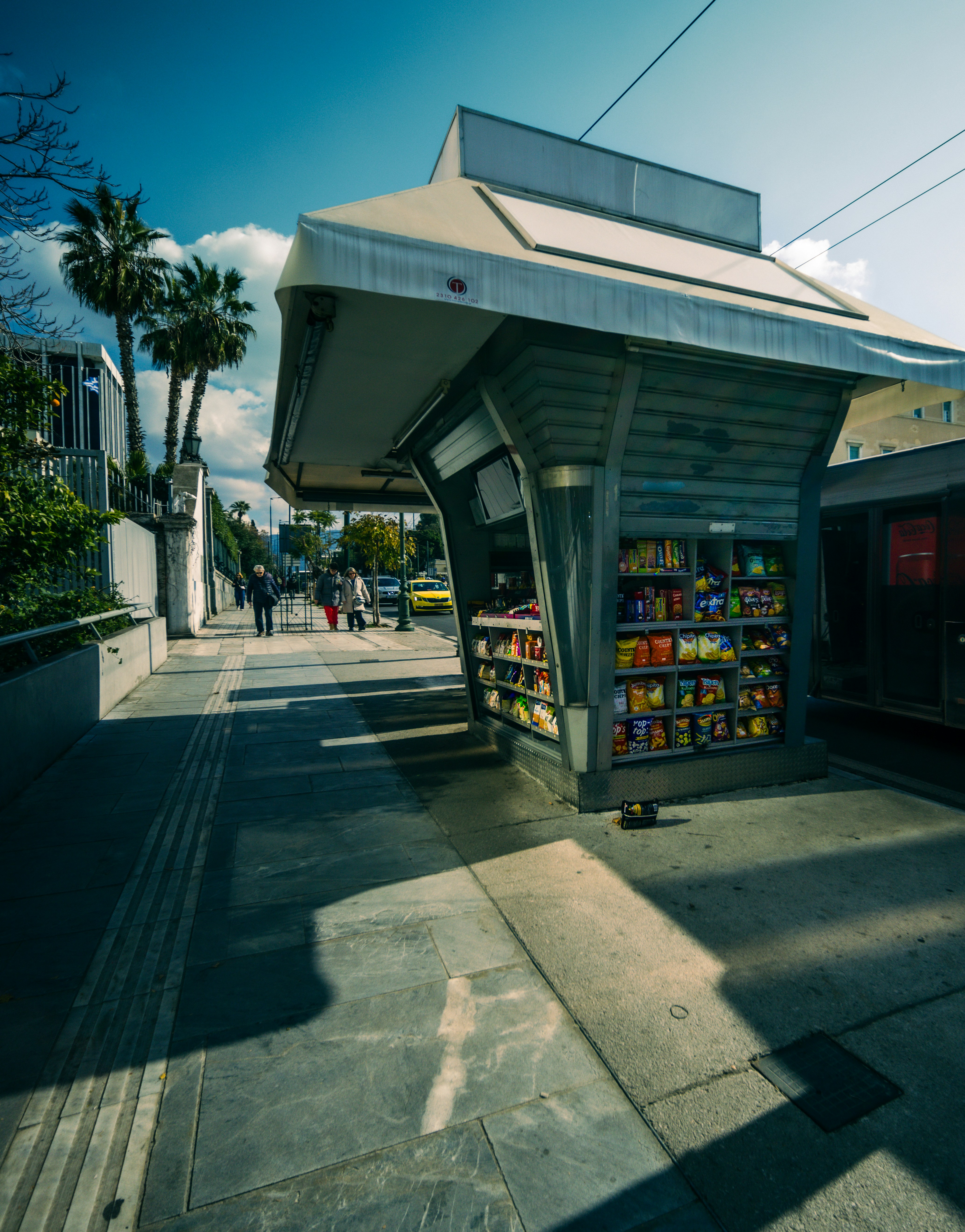 Street kiosk with colorful snack display on a sunny sidewalk.