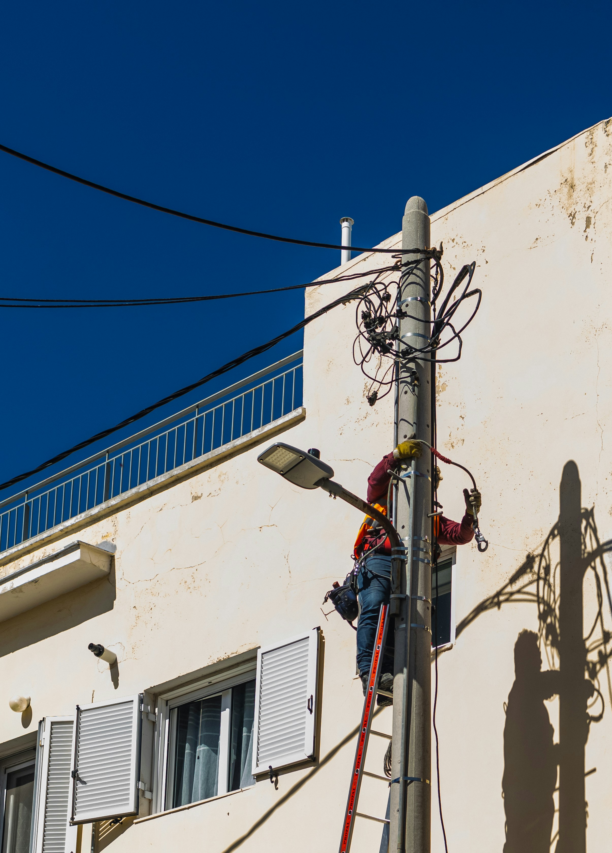 Utility Pole Acrobat: Worker Scaling a Rooftop Power Line