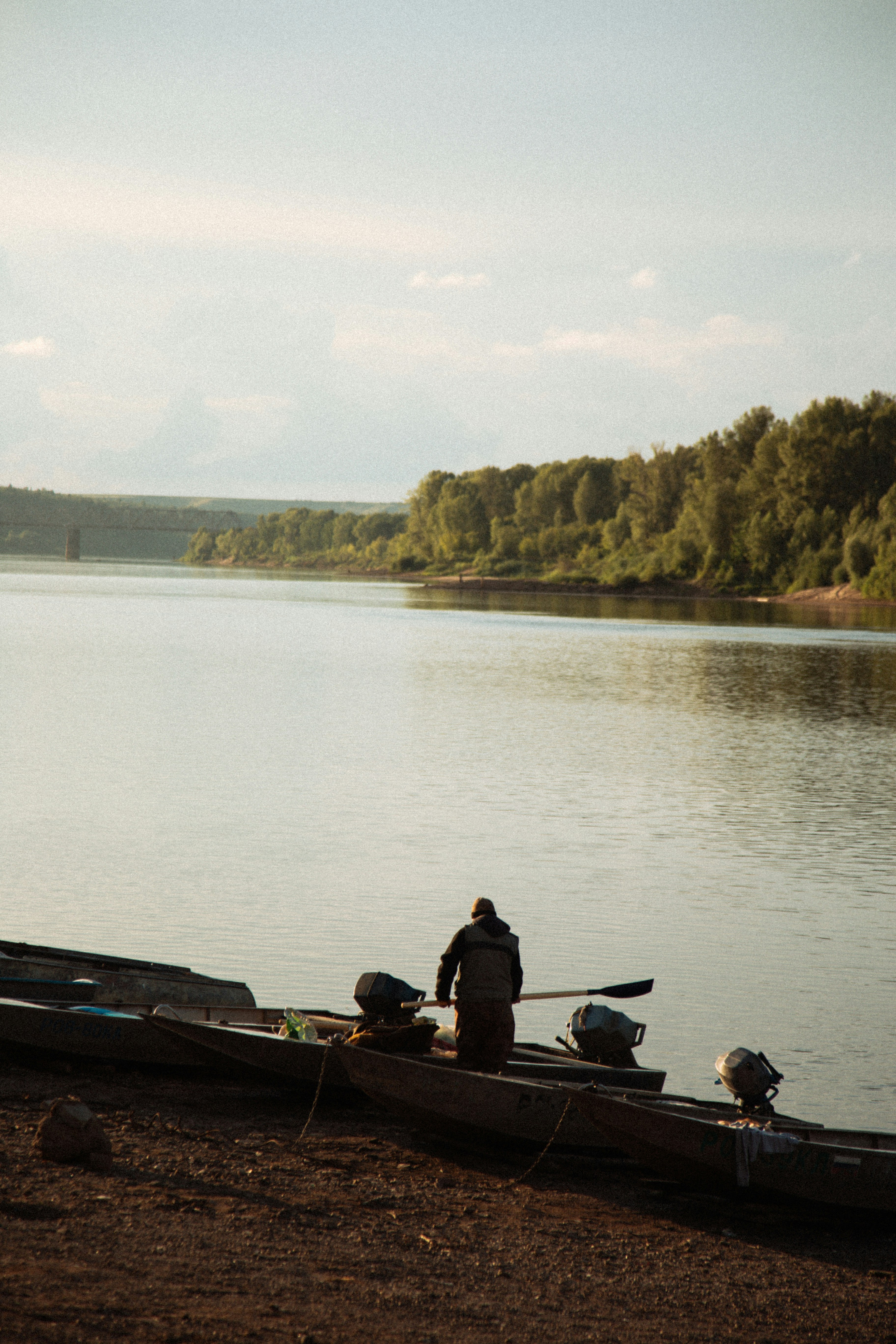 Quiet Currents: A lone paddler by the row of boats along a calm river