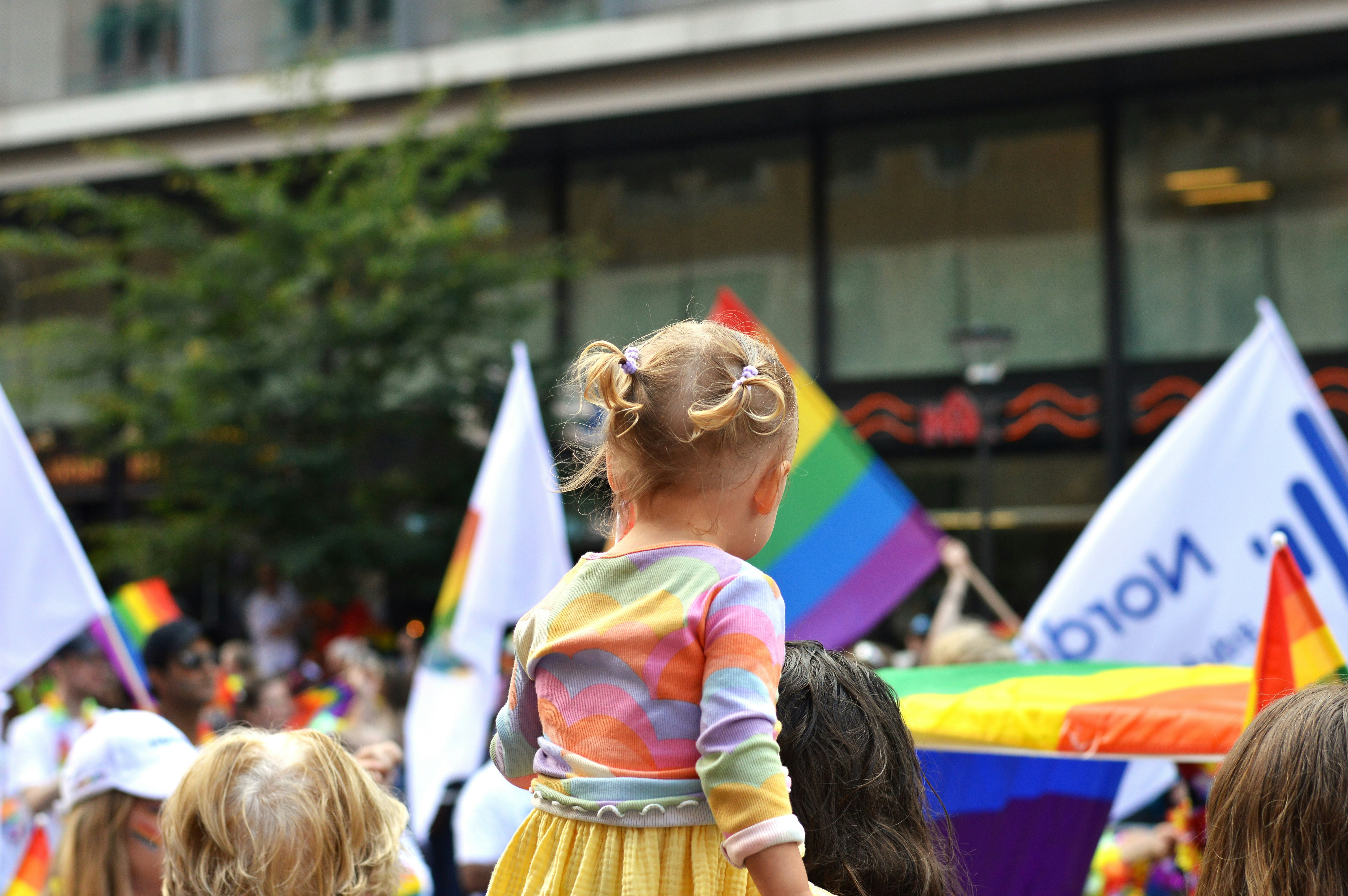 Tiny Rainbow Observer on Shoulders Amid a Pride Parade