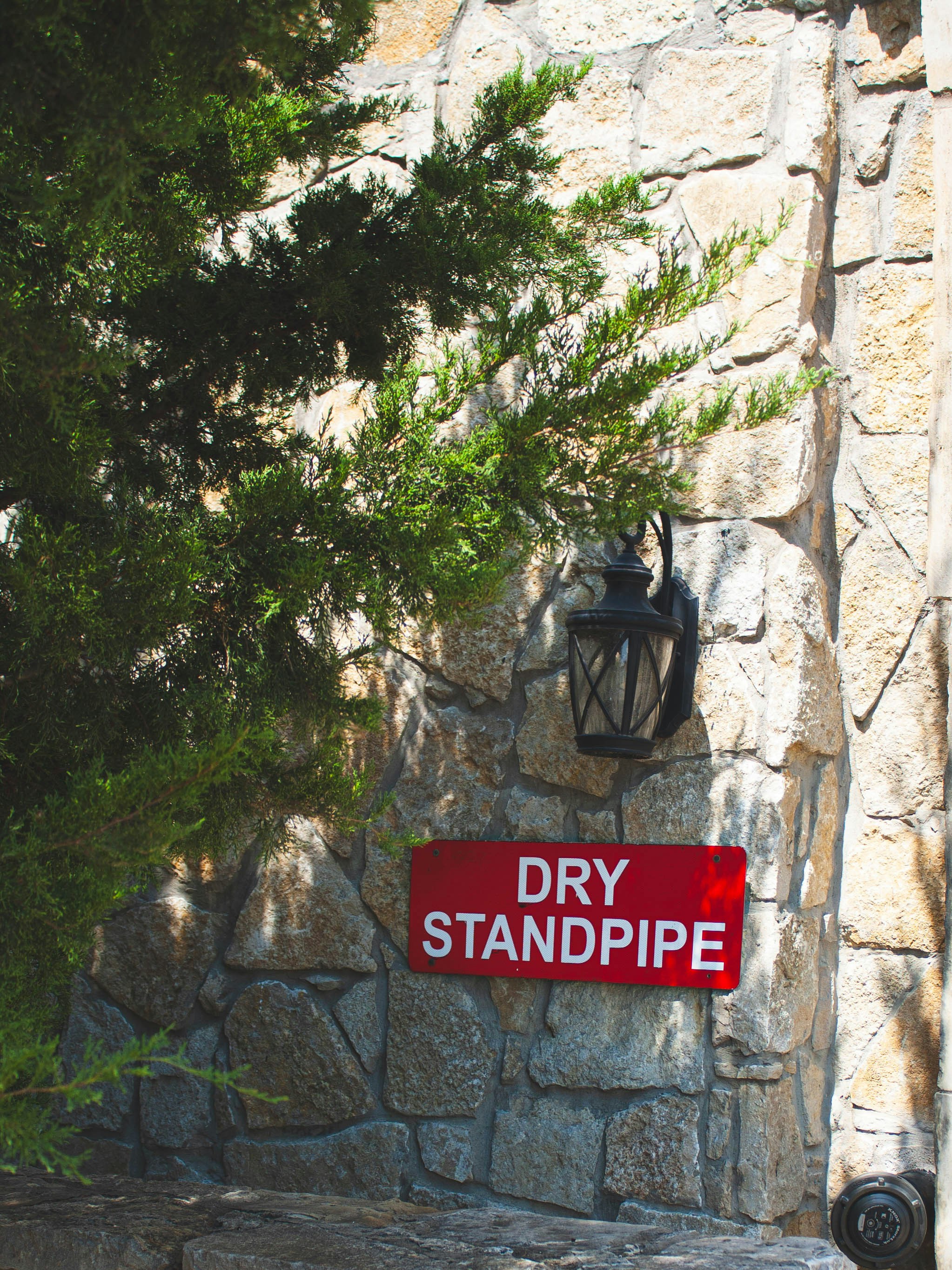 Red Dry Standpipe Sign on Weathered Stone Facade Beneath Lantern Light