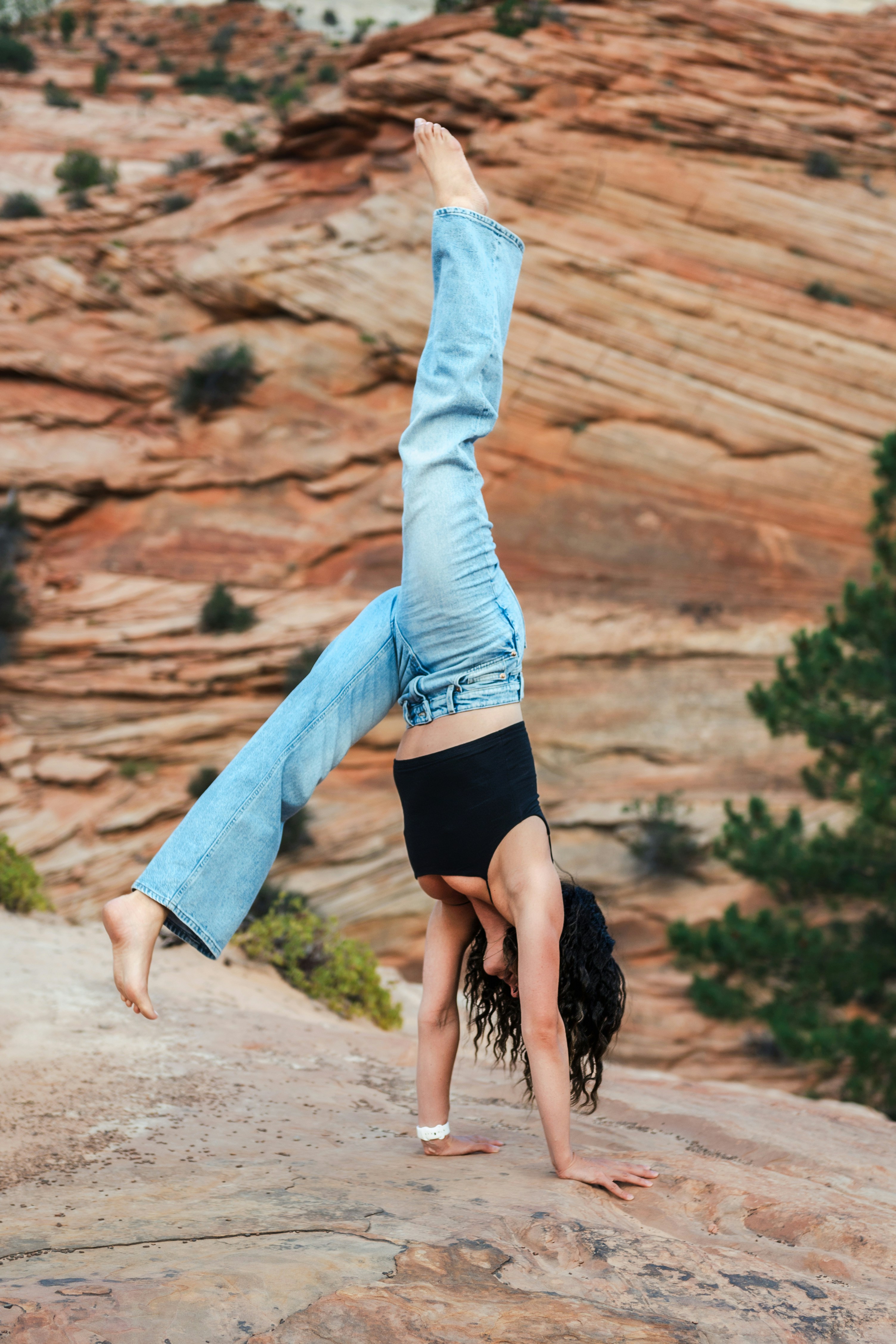Person performing a handstand on rocky terrain with layered stone formations in the background.