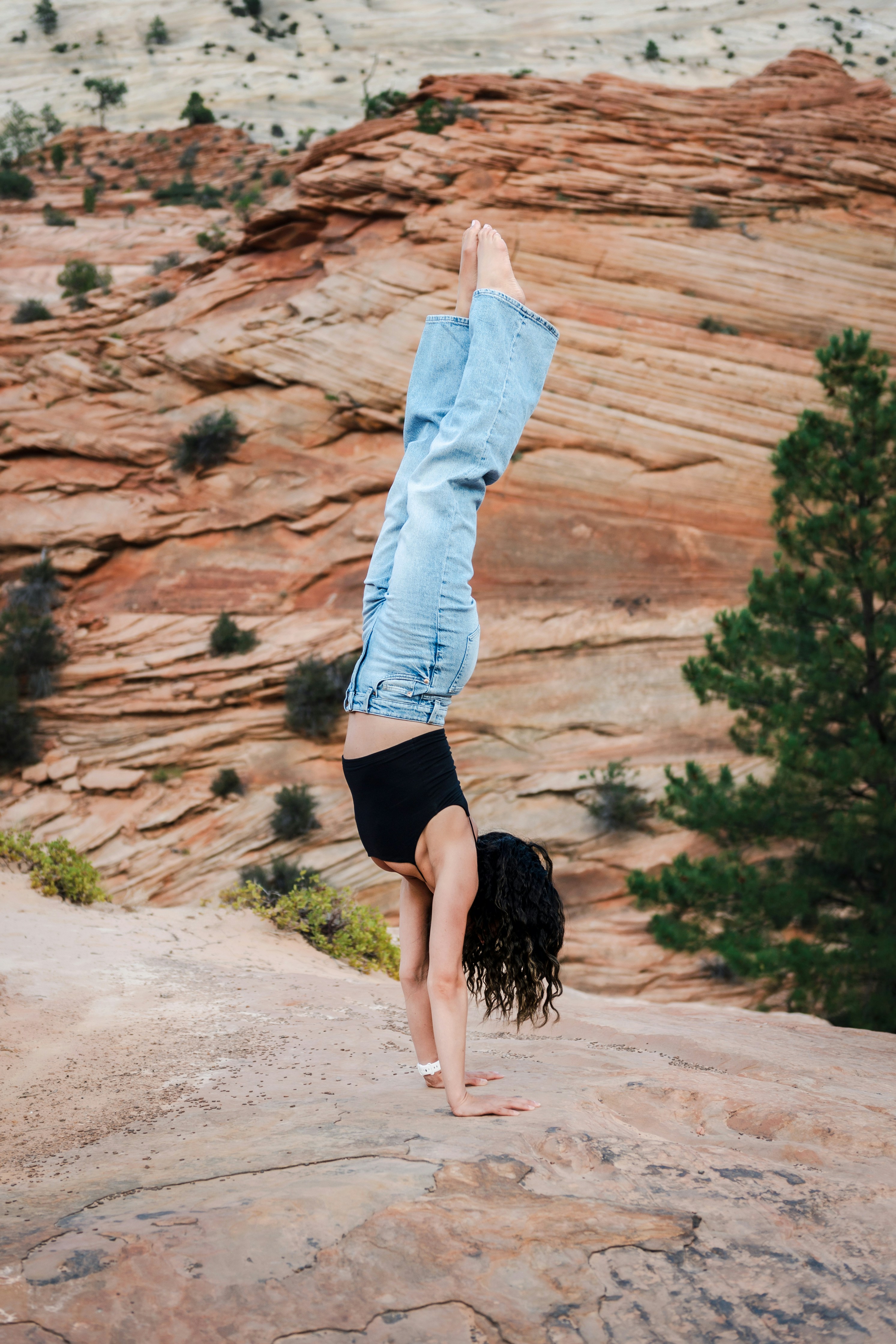 Person performing a handstand on a rocky cliff with layered sandstone formations in the background.