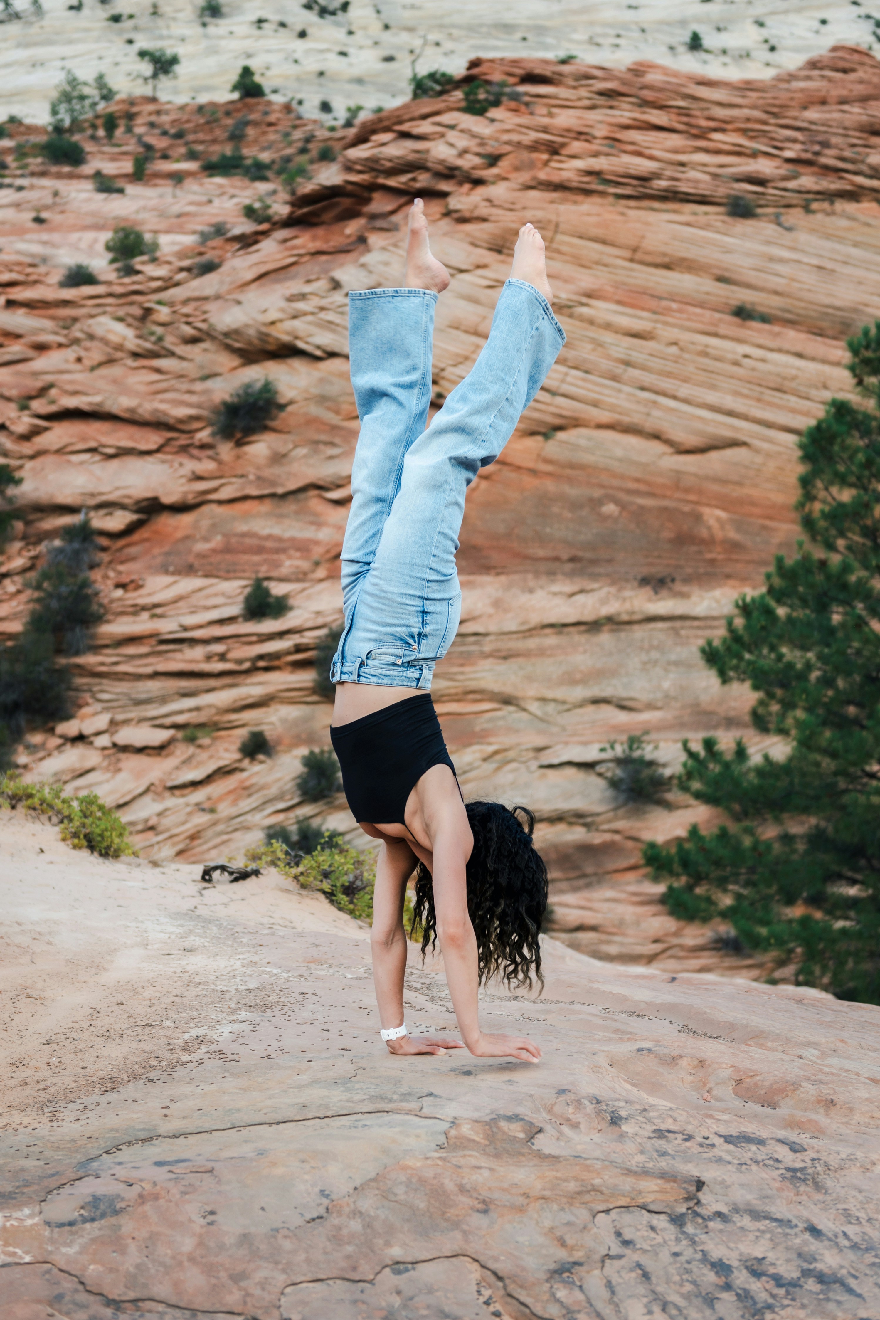 Person performing a handstand on a rocky landscape with layered sandstone formations.