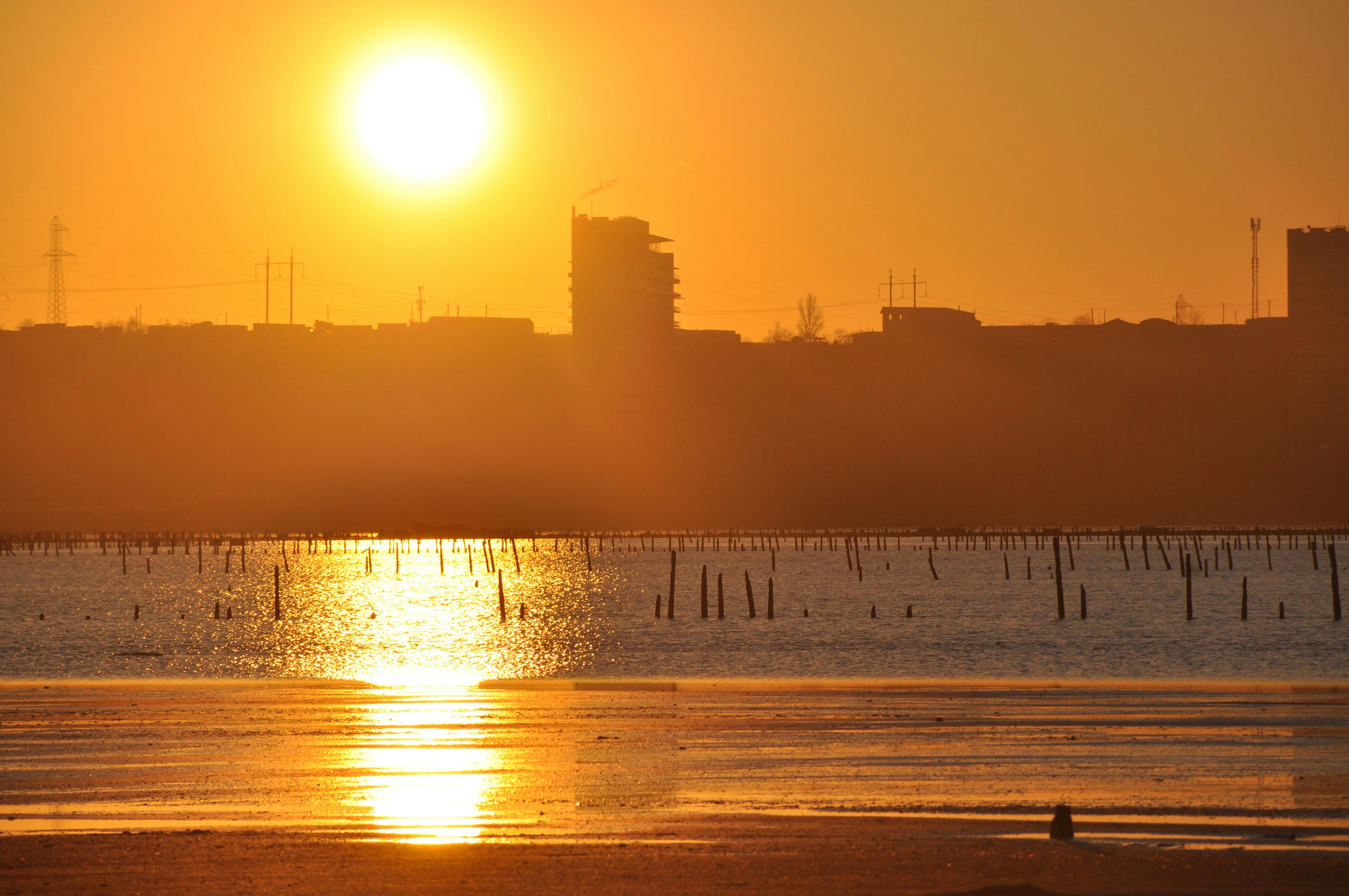 Sunset casting a warm glow over the silhouette of a city skyline and reflective water surface.