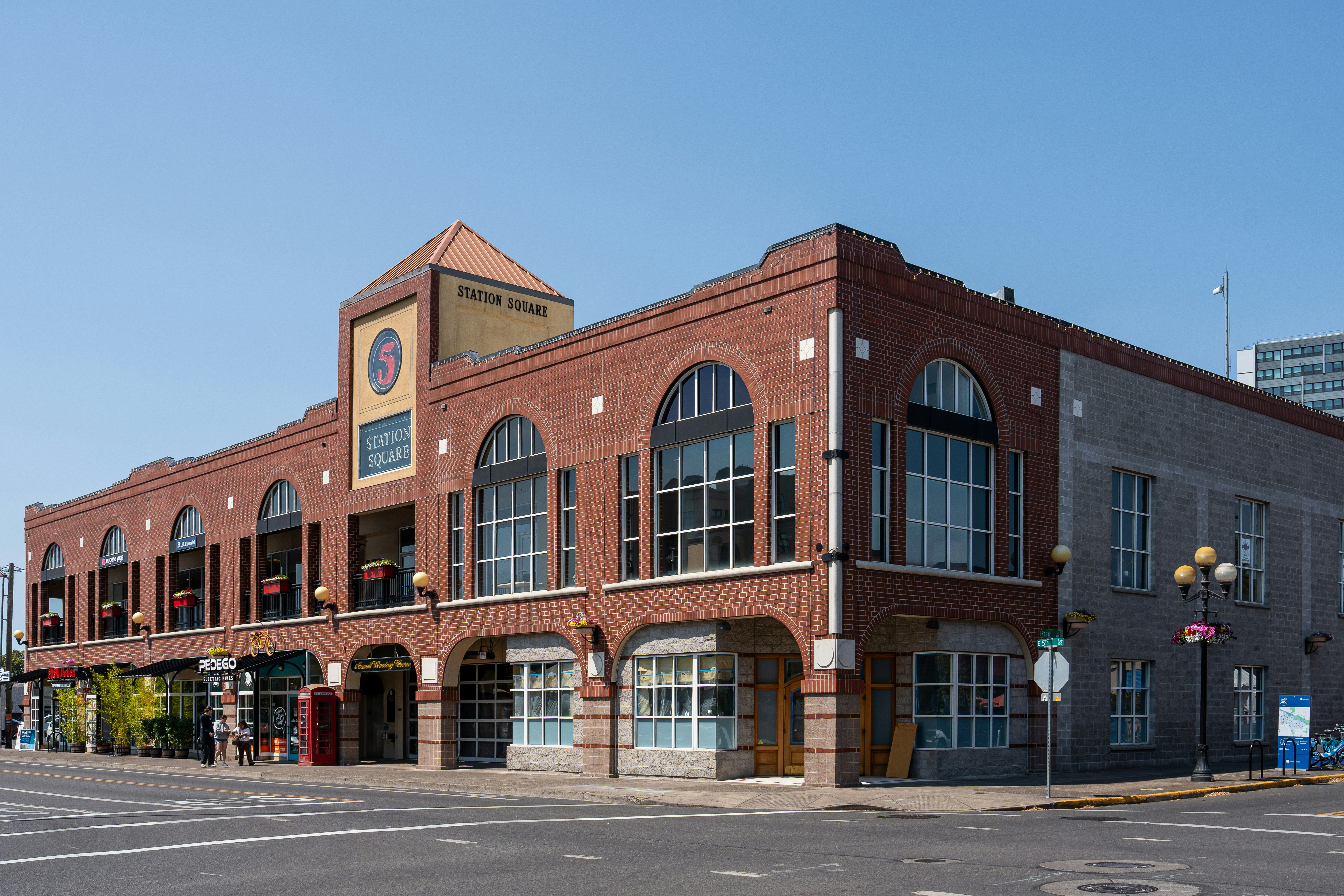 Large two-story brick building with arched windows and a corner tower under a clear blue sky.
