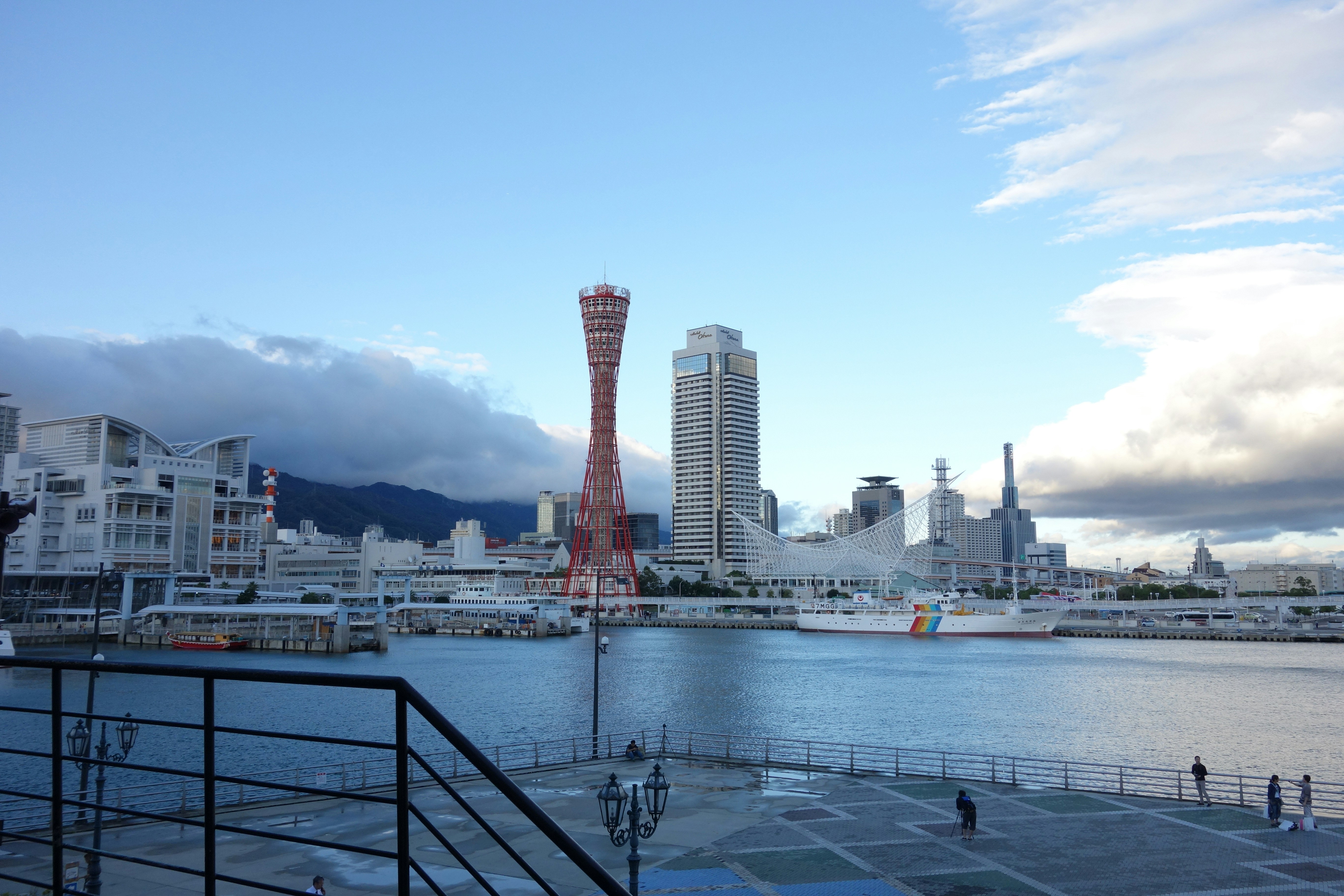 Modern skyline with a distinctive red tower against a backdrop of mountains and dramatic clouds.