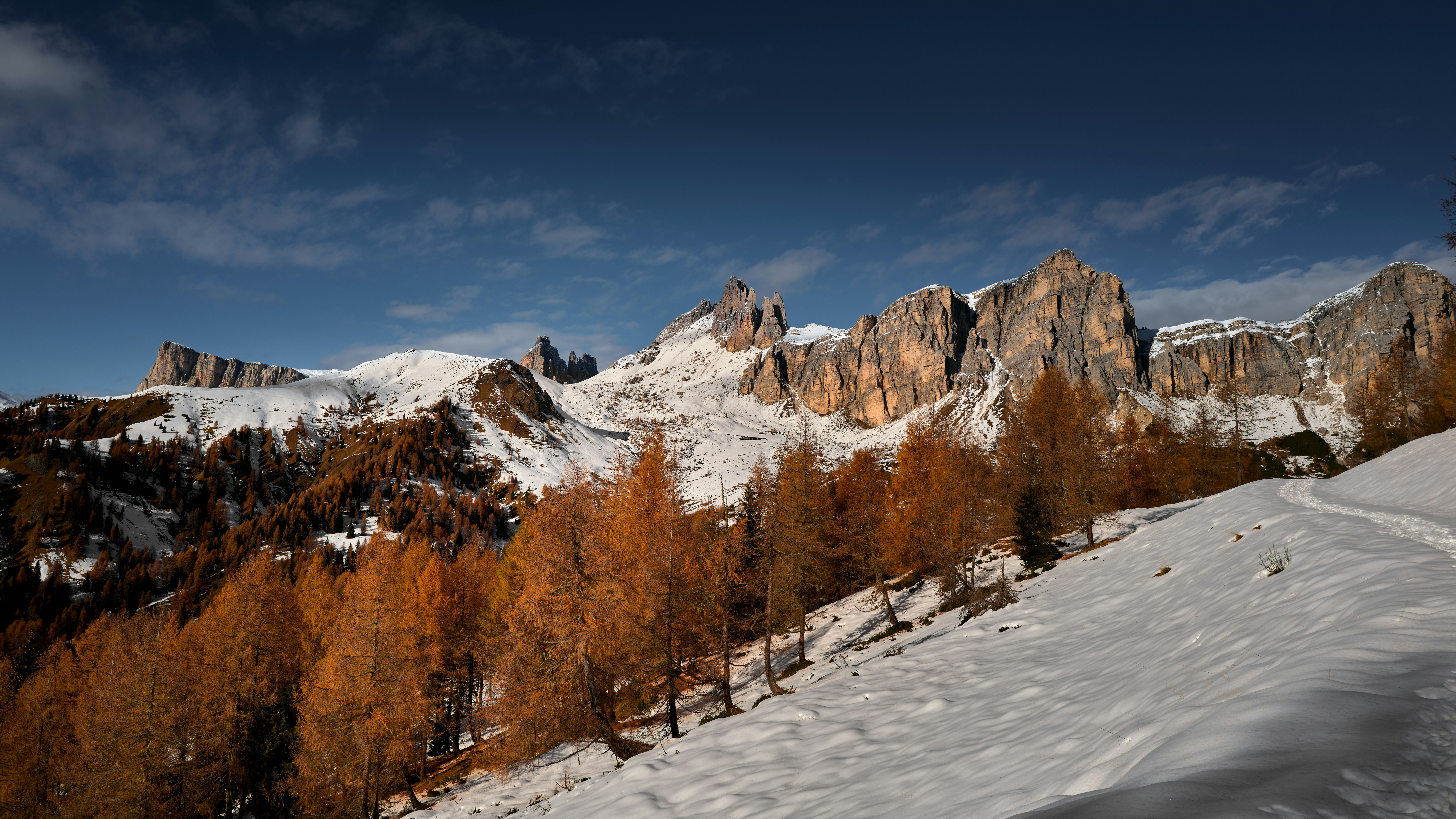 Snow-dusted Dolomite peaks with golden autumn trees under a clear blue sky.