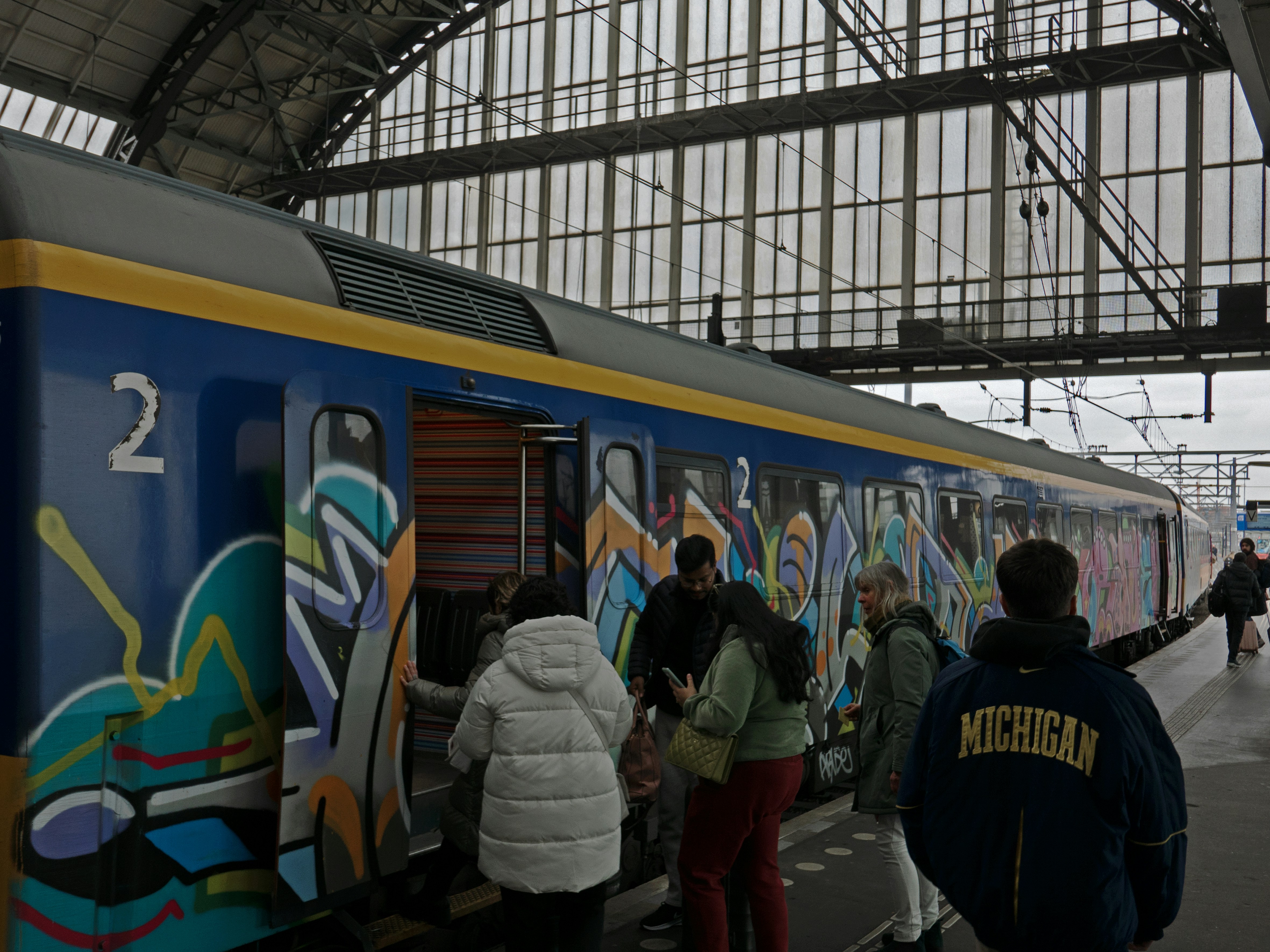Color on Rails: Passengers Converge Before a Graffiti-Wrapped Train at a Glass-Arched Platform