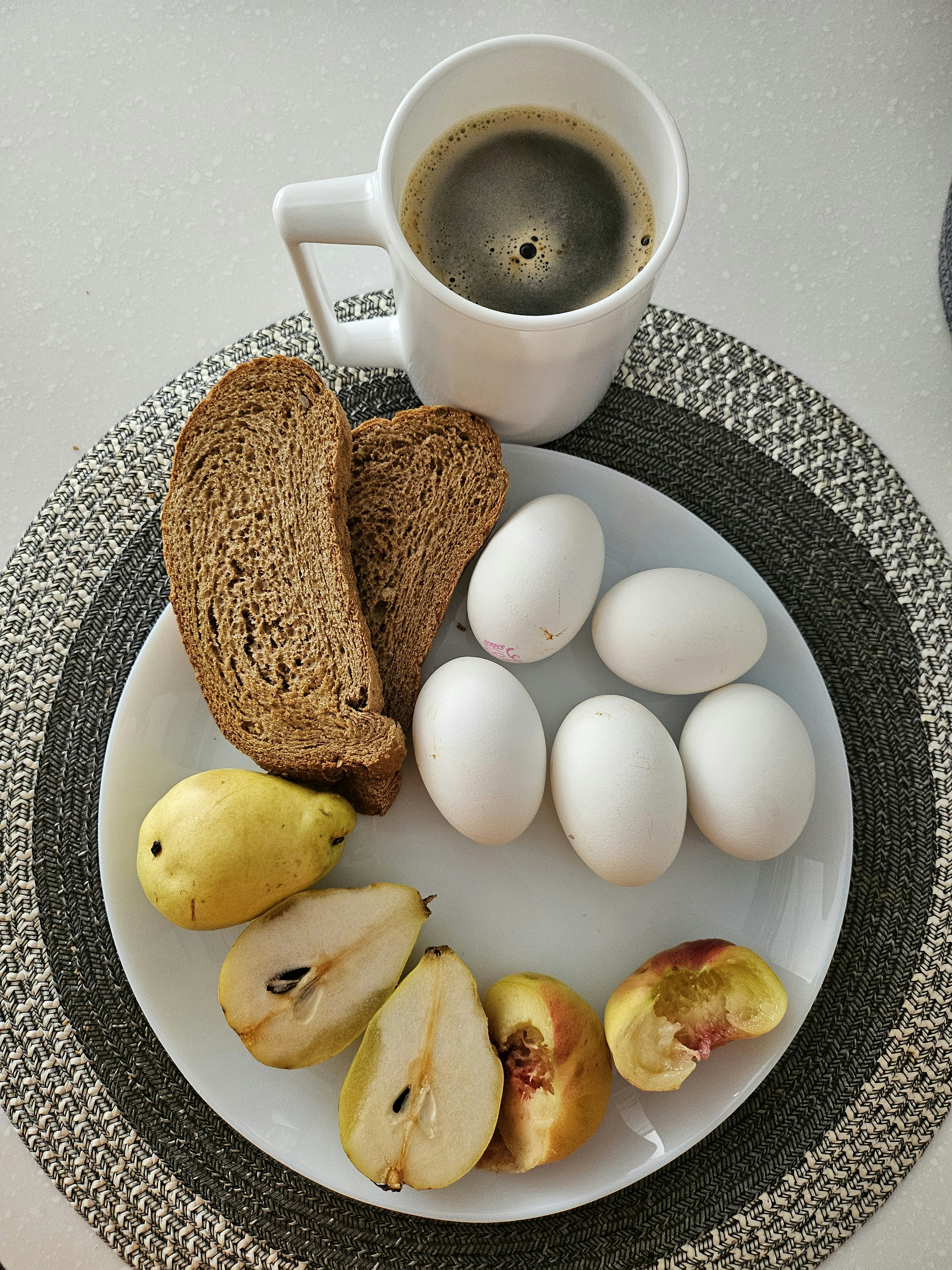A photograph of a breakfast arrangement featuring toast, white eggs, pears, and a cup of coffee on a textured plate.