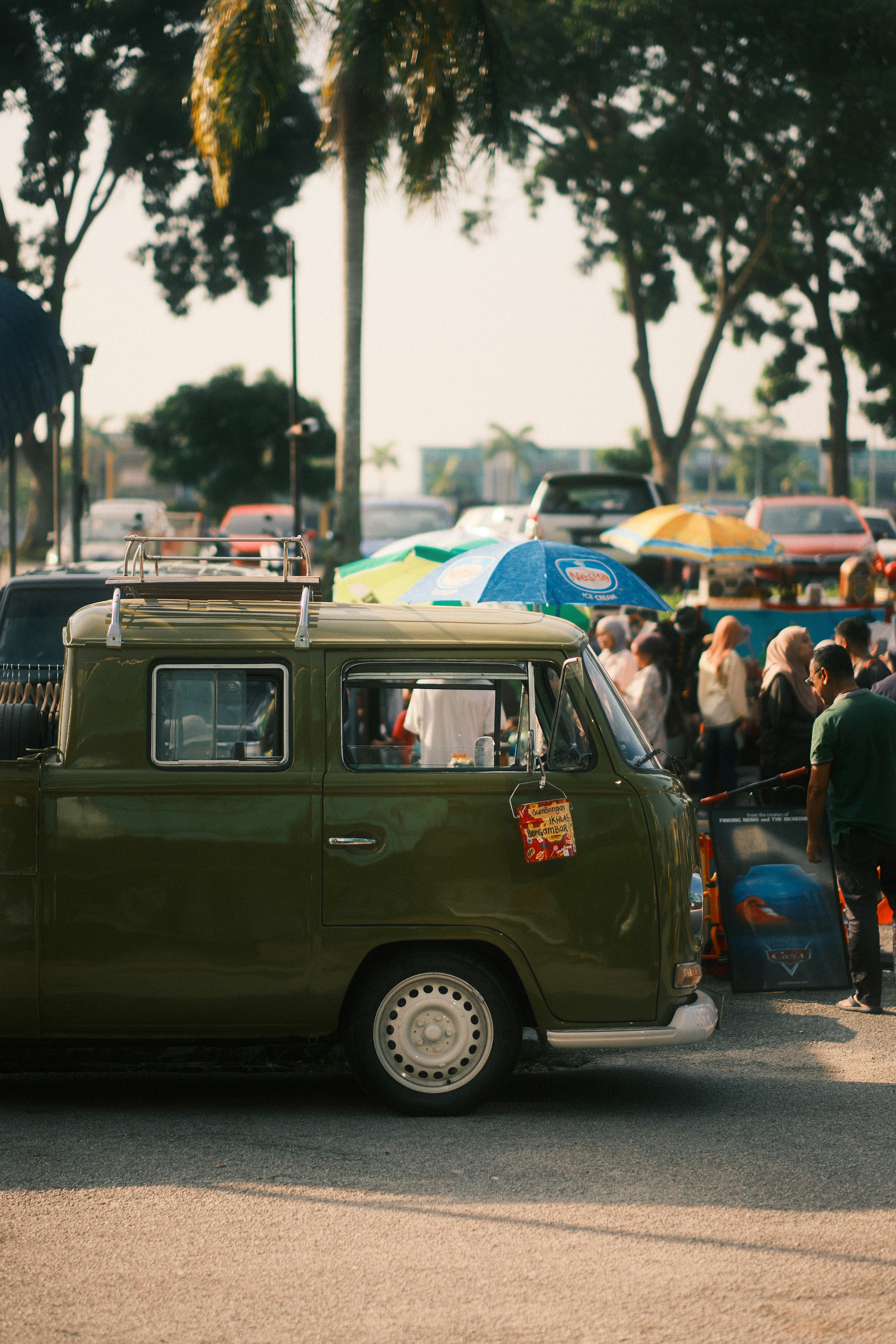 A small green van driving down a street next to a crowd of people photo ...