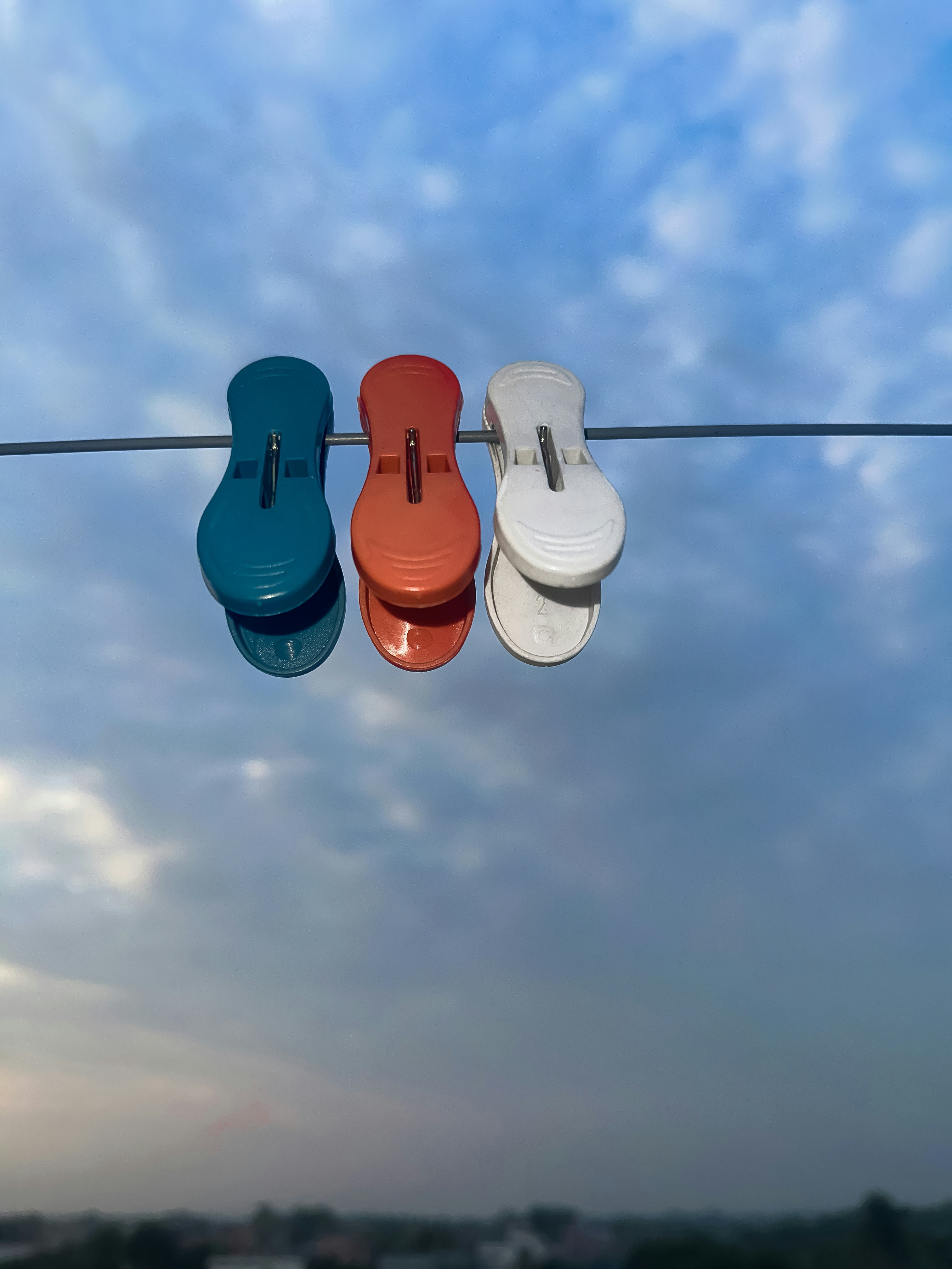 Three Coated Clothespins on a Wire Against a Sky