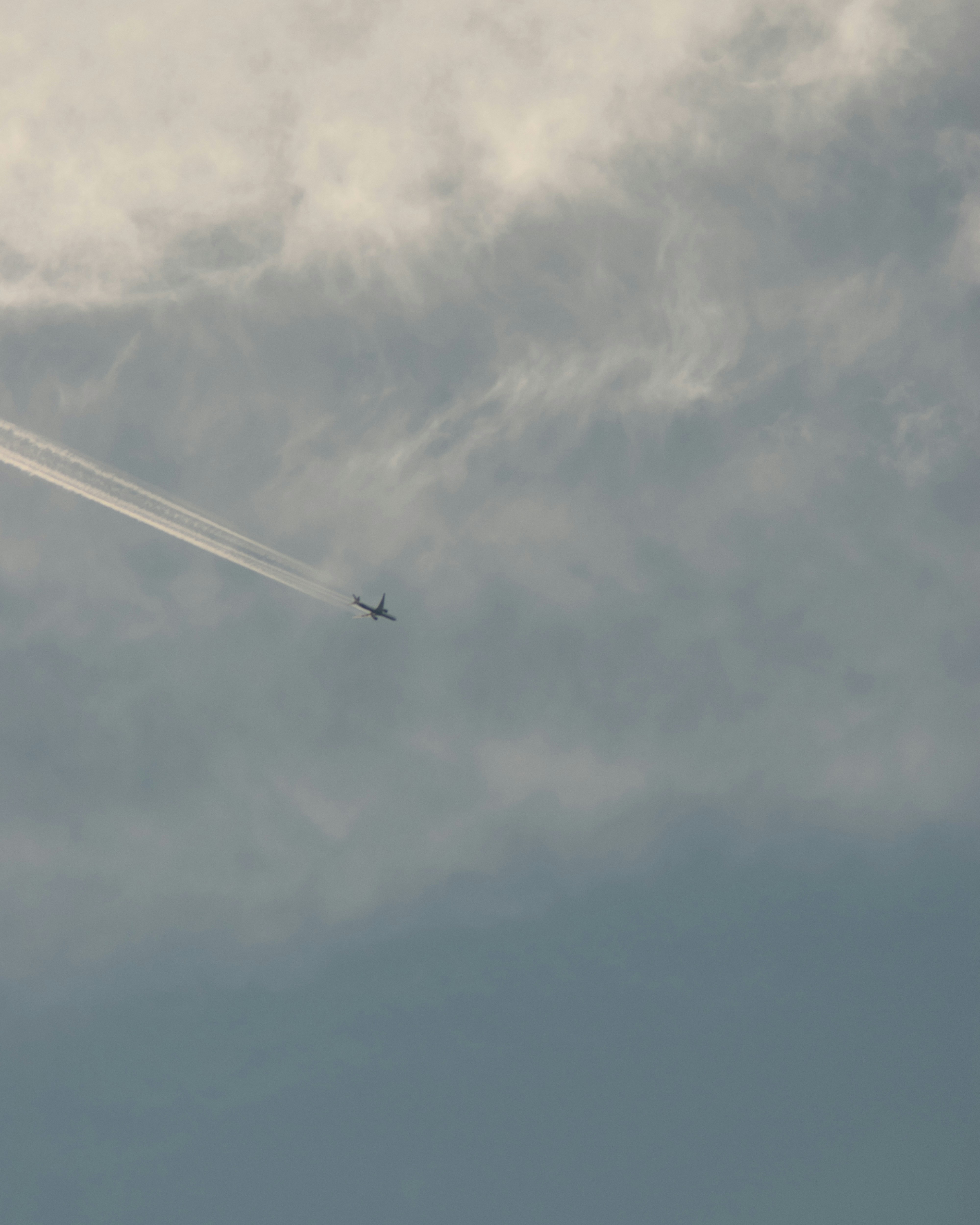 Aerial Brushstroke: a lone plane carves a diagonal contrail through pale sky