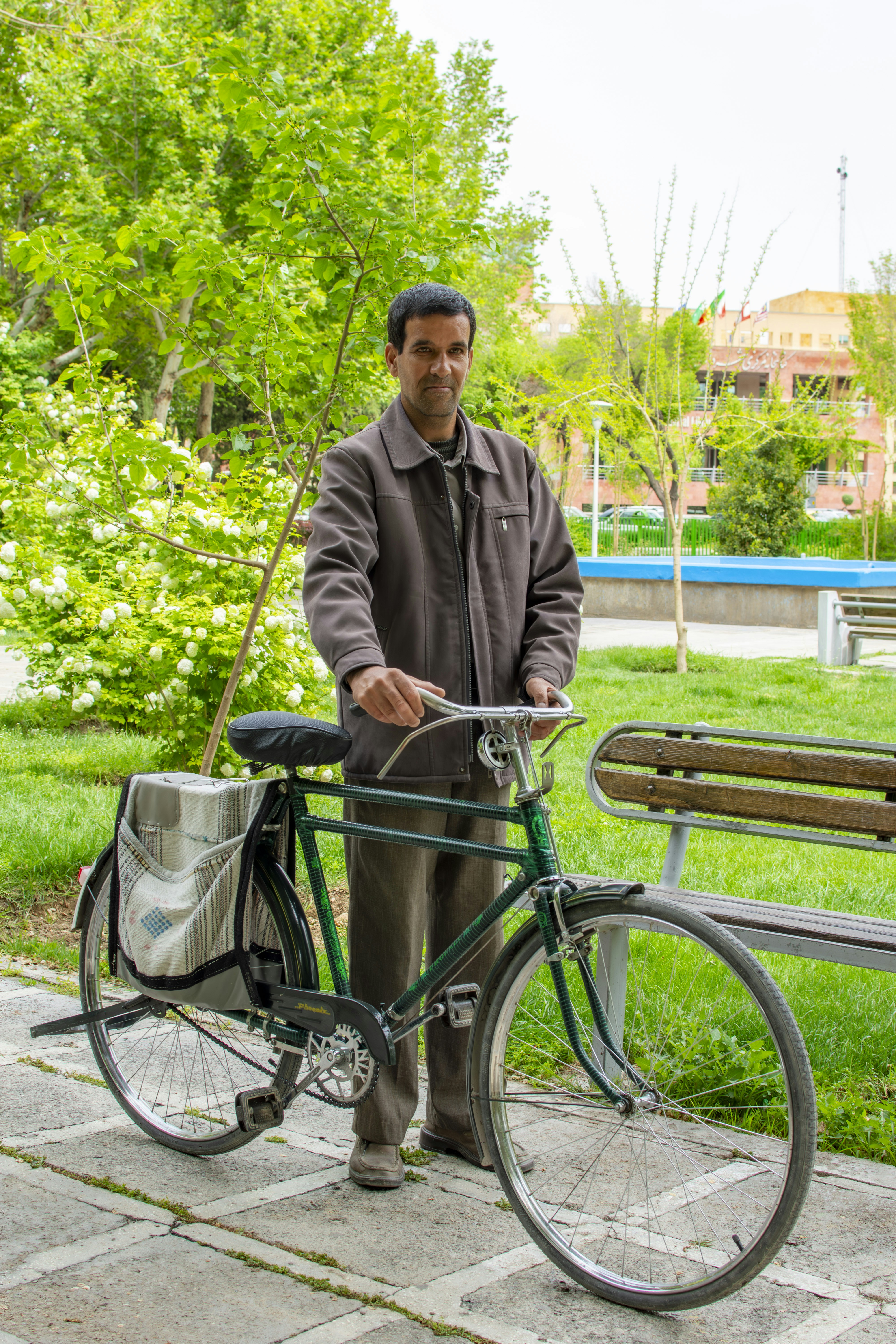 Green-tinged Pause: A man with a vintage bicycle by a sunlit park bench