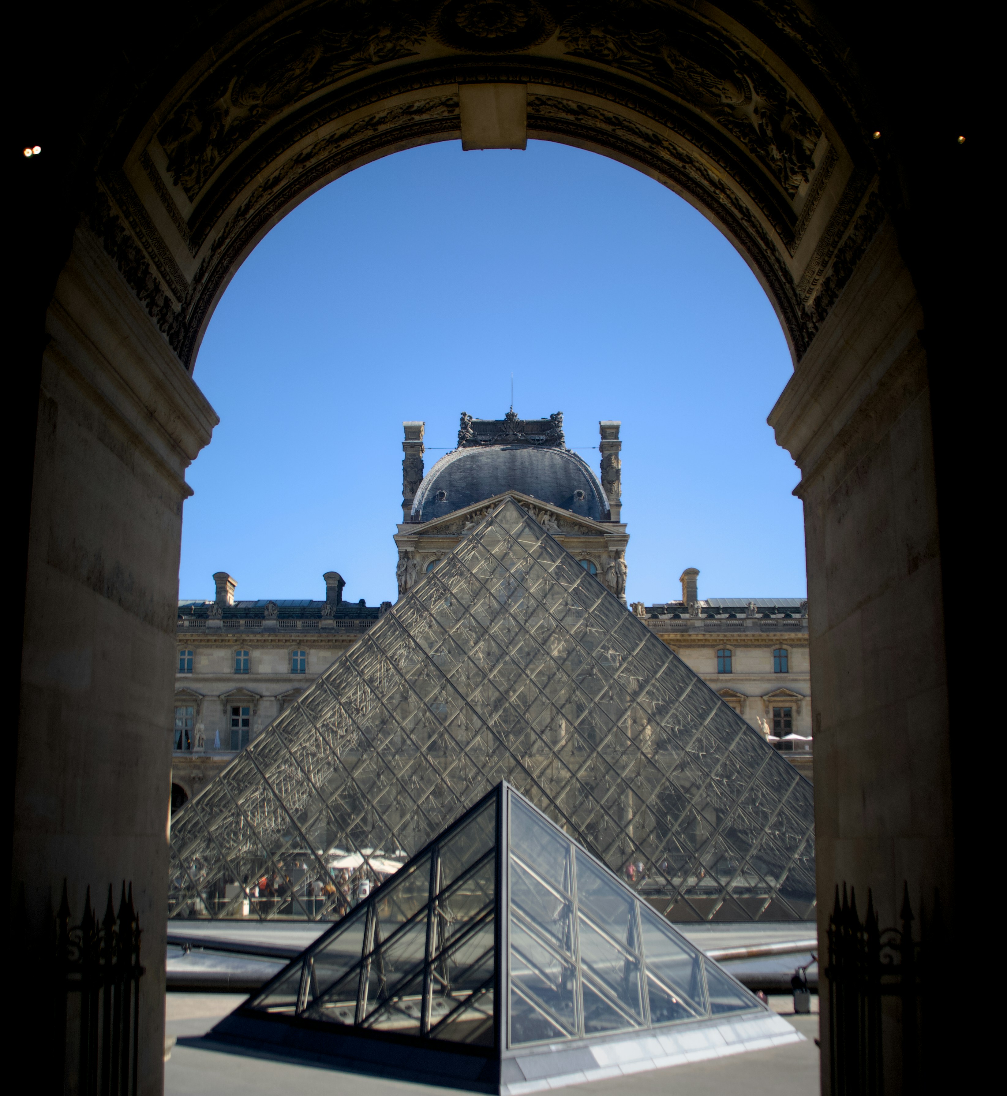 Under the Arch: The Louvre Pyramid Framed in Shadow Against a Bright Sky