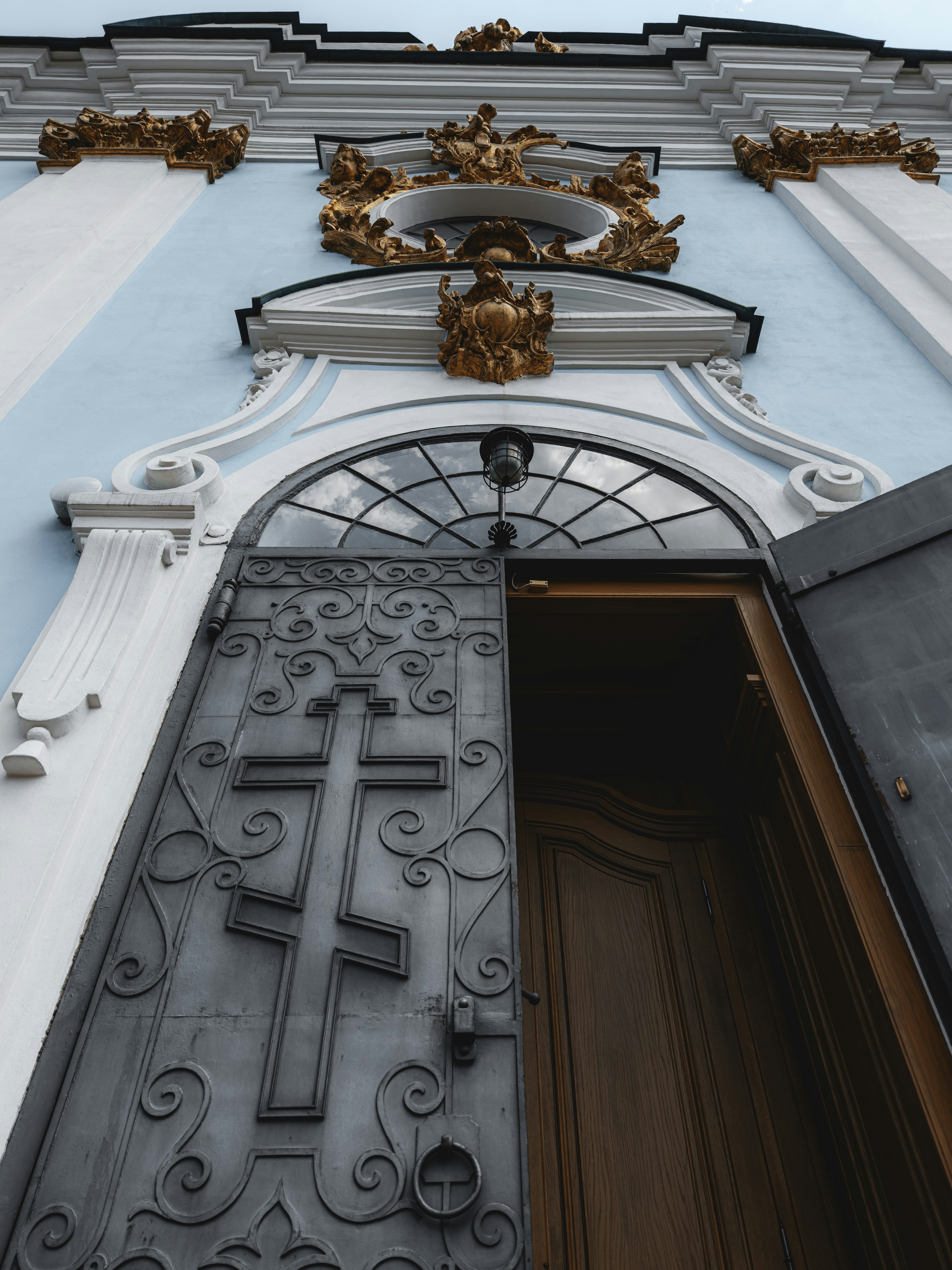 Ornate church portal: turquoise facade, carved crest, and heavy iron door