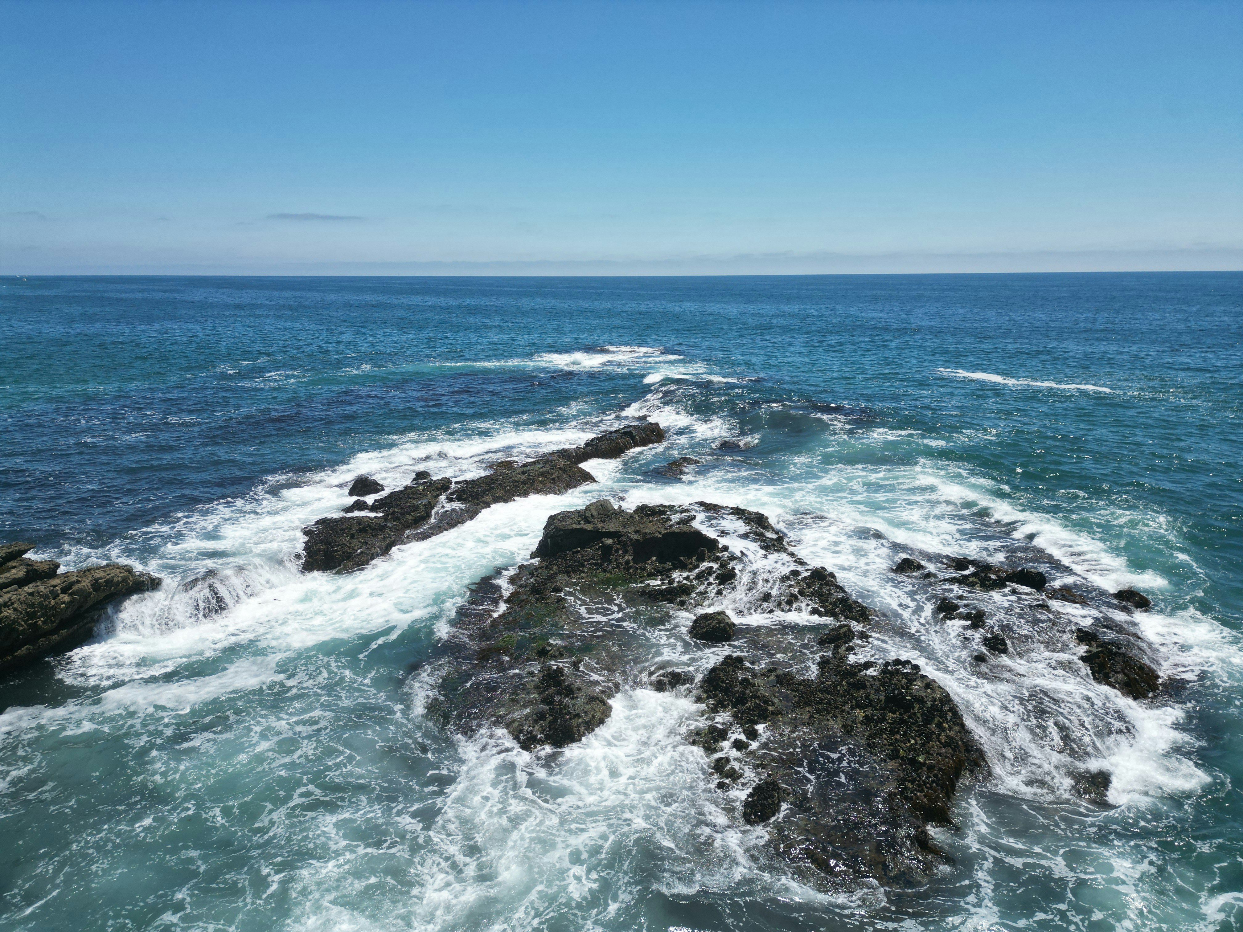 Waves crashing against rugged rocks below a clear blue sky.