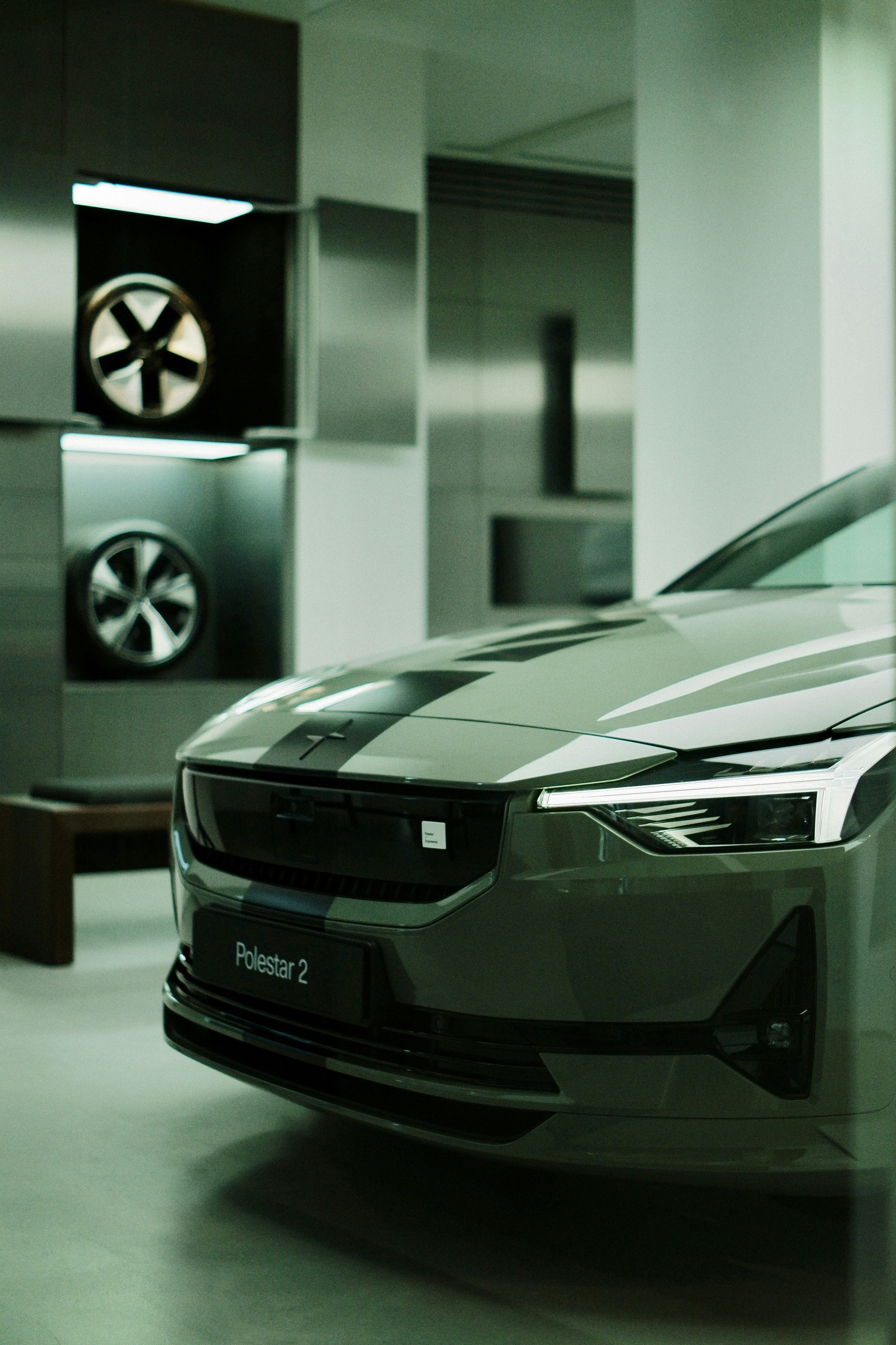 Polestar 2 displayed in a contemporary showroom with alloy wheels featured on the wall.