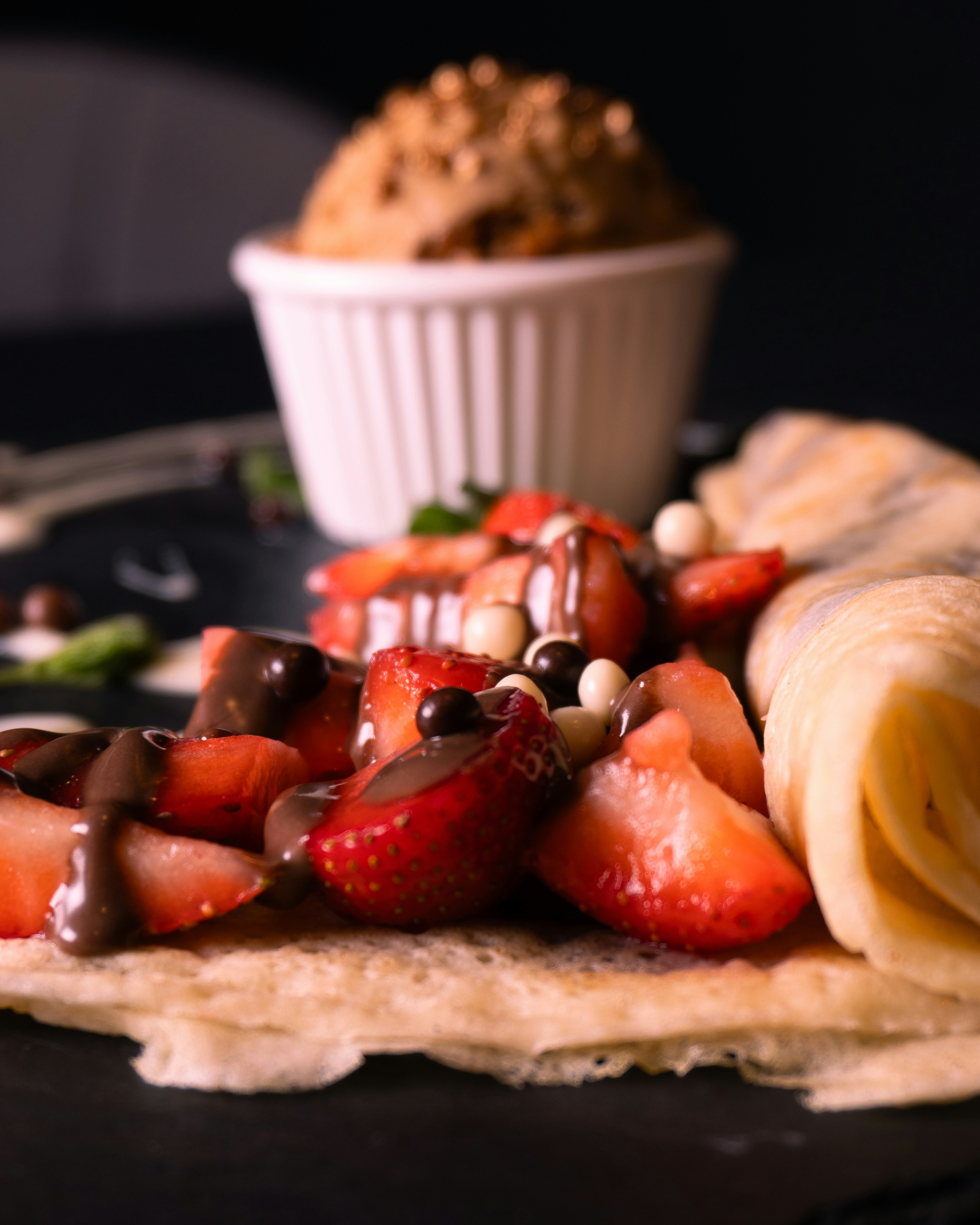 Crimson Strawberry Mosaic on a Chocolate-Drizzled Crepe, Framed by a Soft-Focus Muffin Backdrop