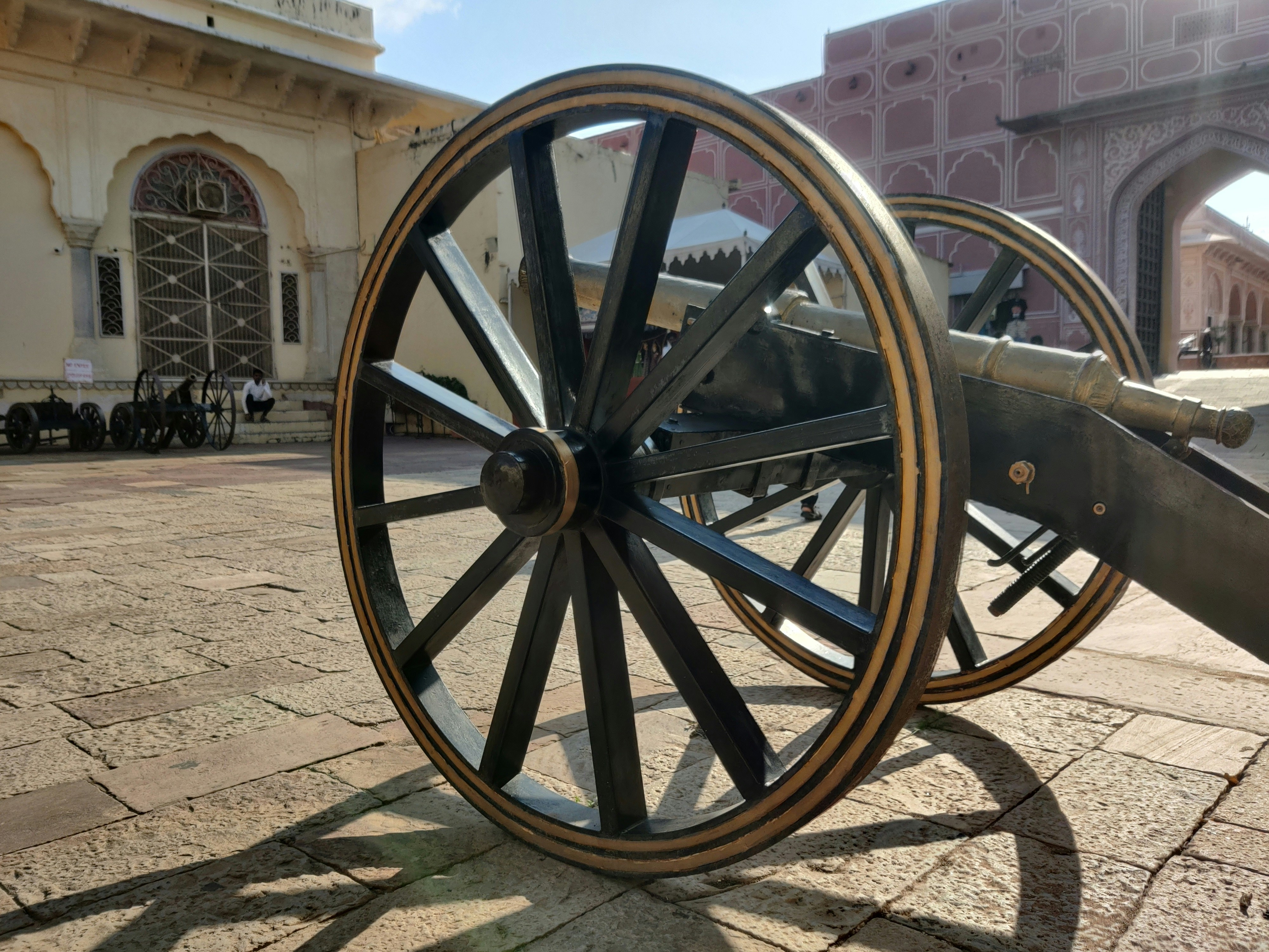 Old cannon wheel casting shadows on a sunlit cobblestone courtyard.
