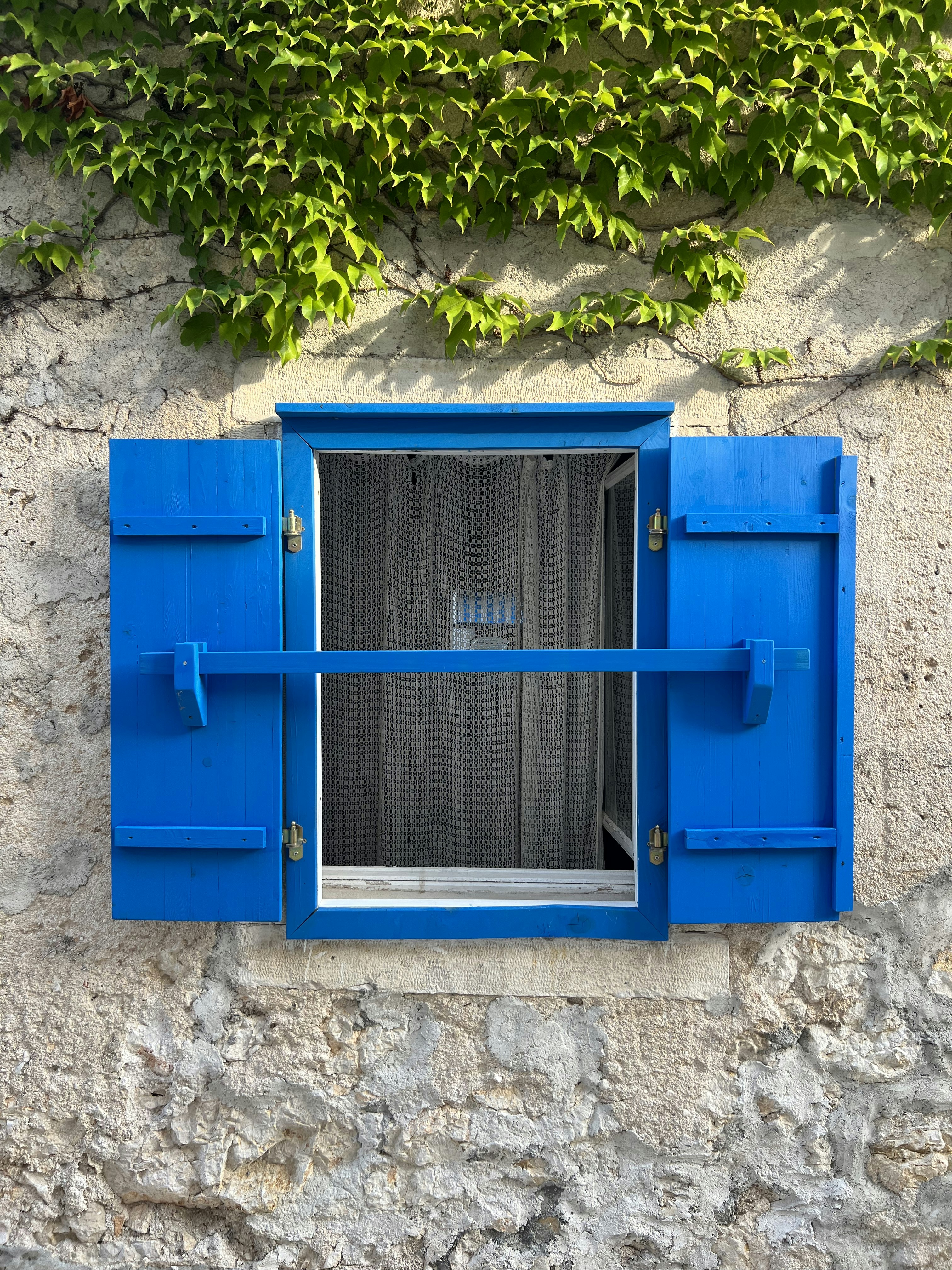Azure Shutters Framing a Sunlit Stone Window on an Ivy-Draped Wall