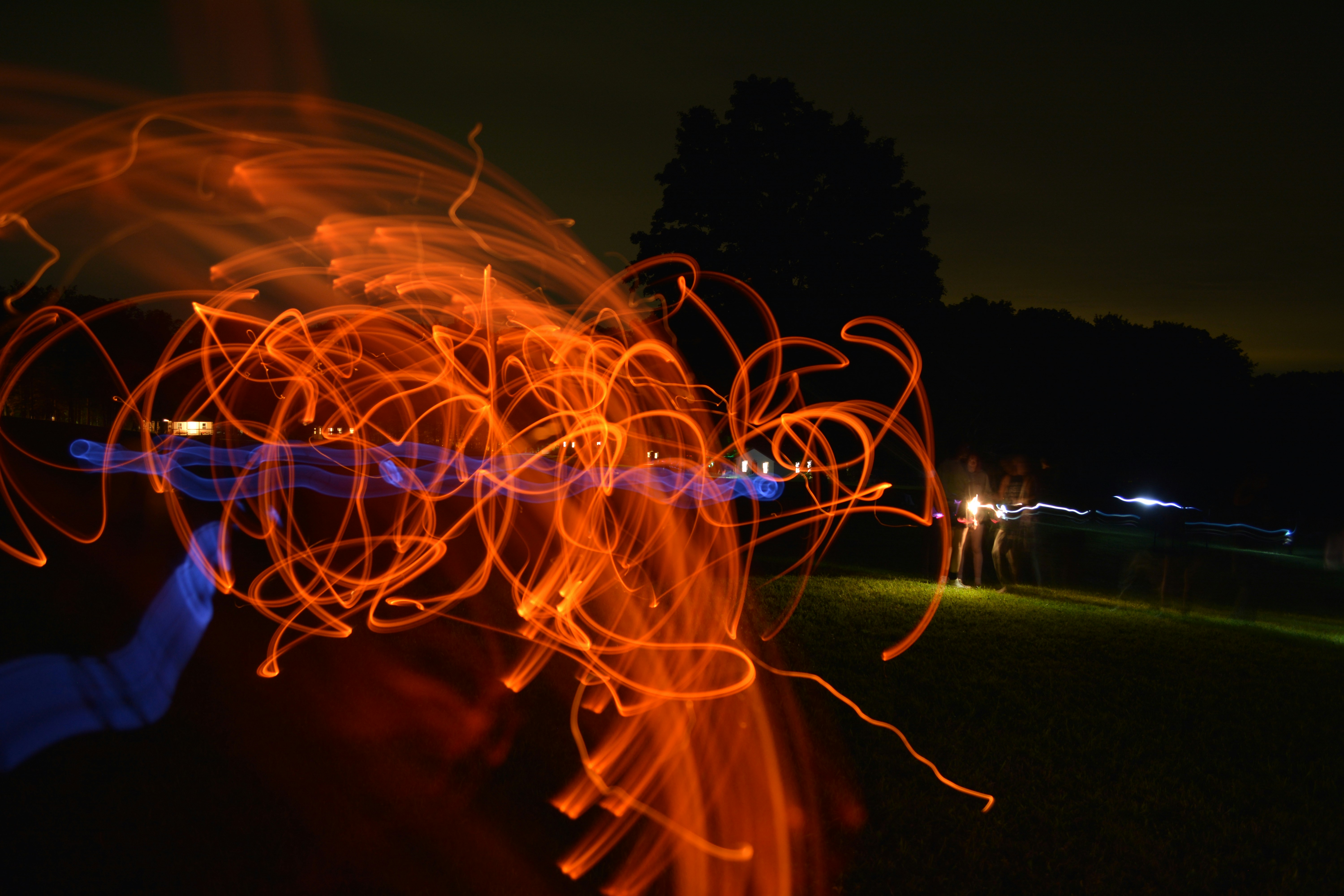 Long exposure of swirling orange lights against a dark outdoor background with trees.