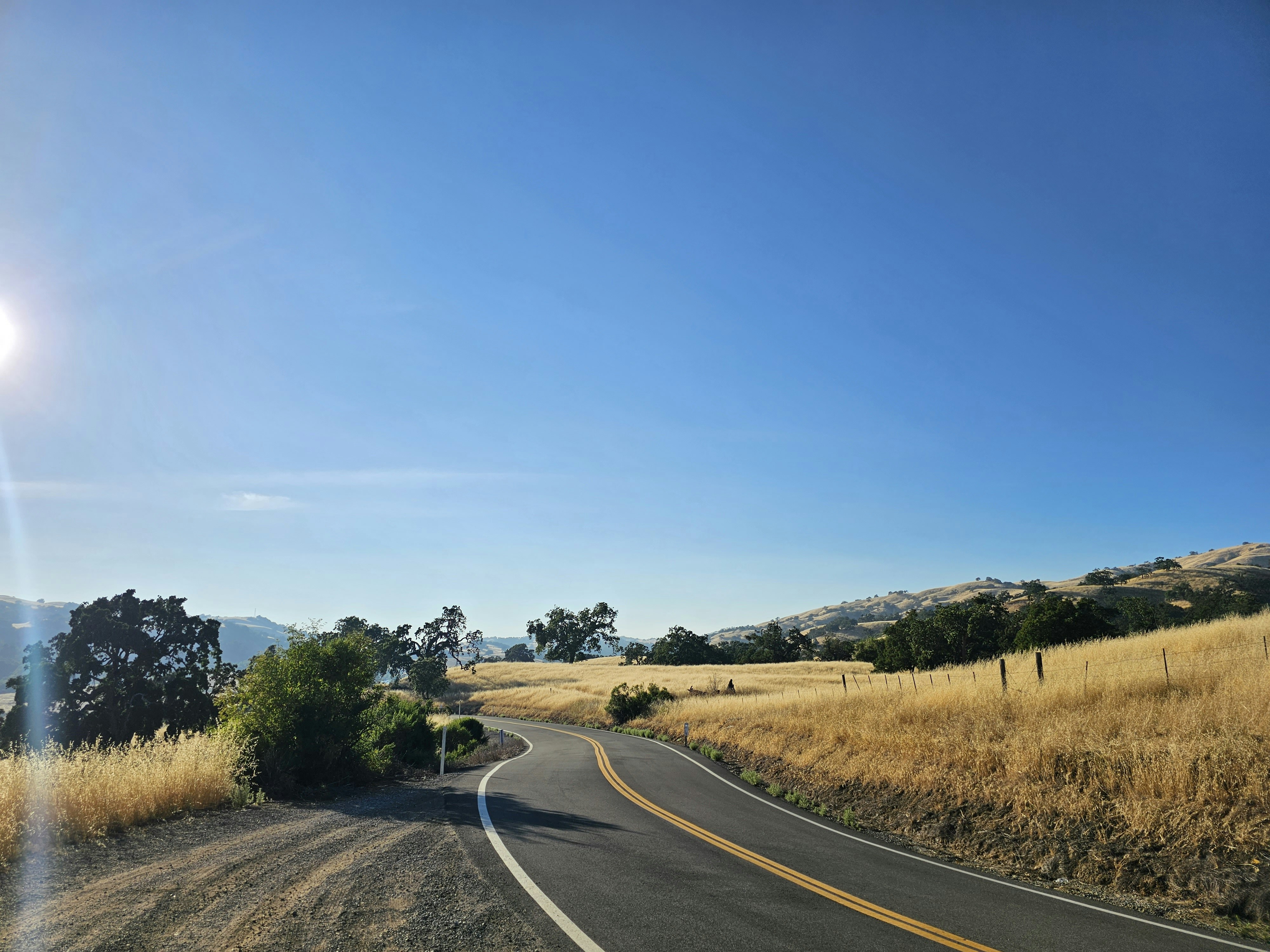 Winding road through dry, golden hills under a clear blue sky.