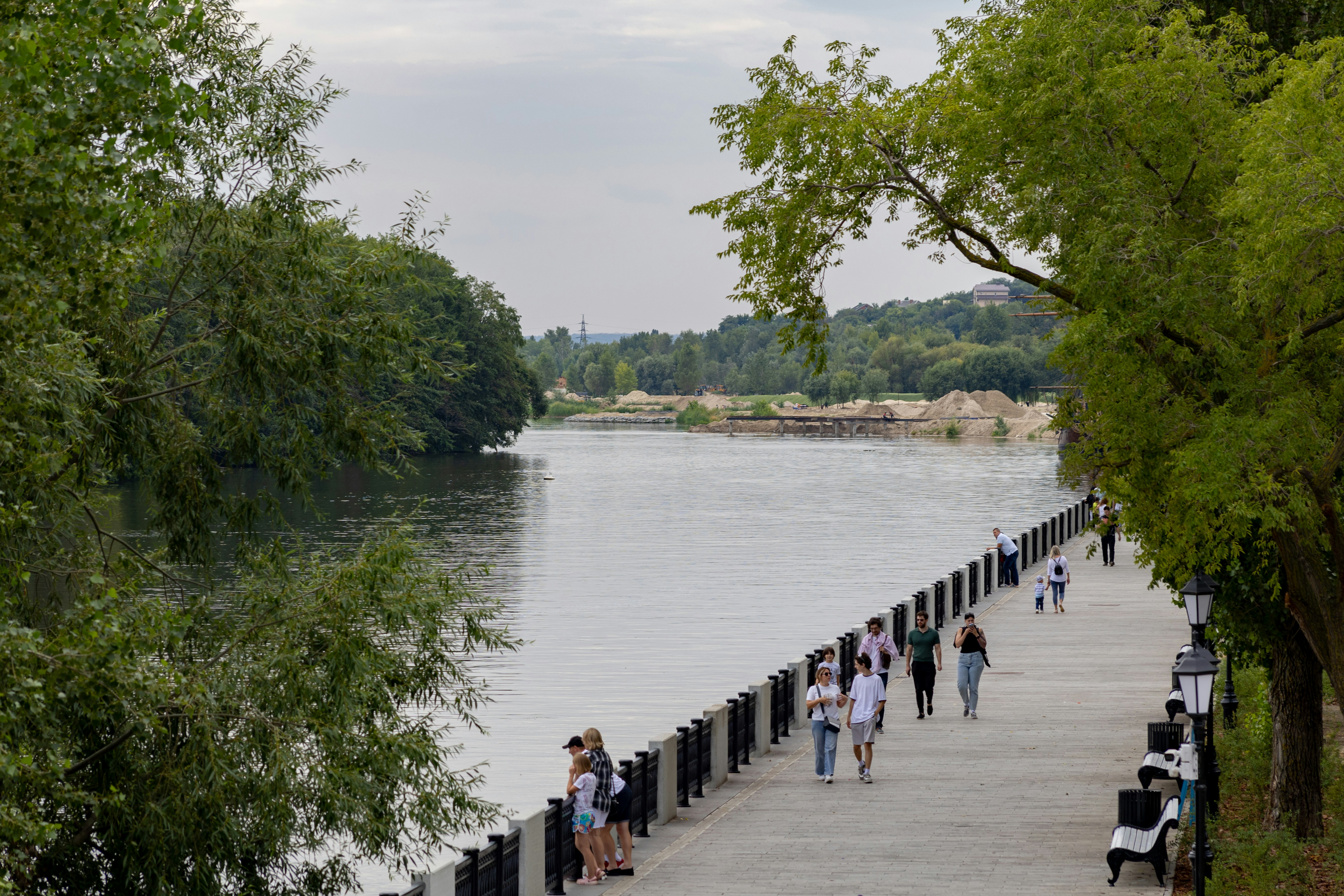 A group of people walking down a sidewalk next to a river photo – Free ...