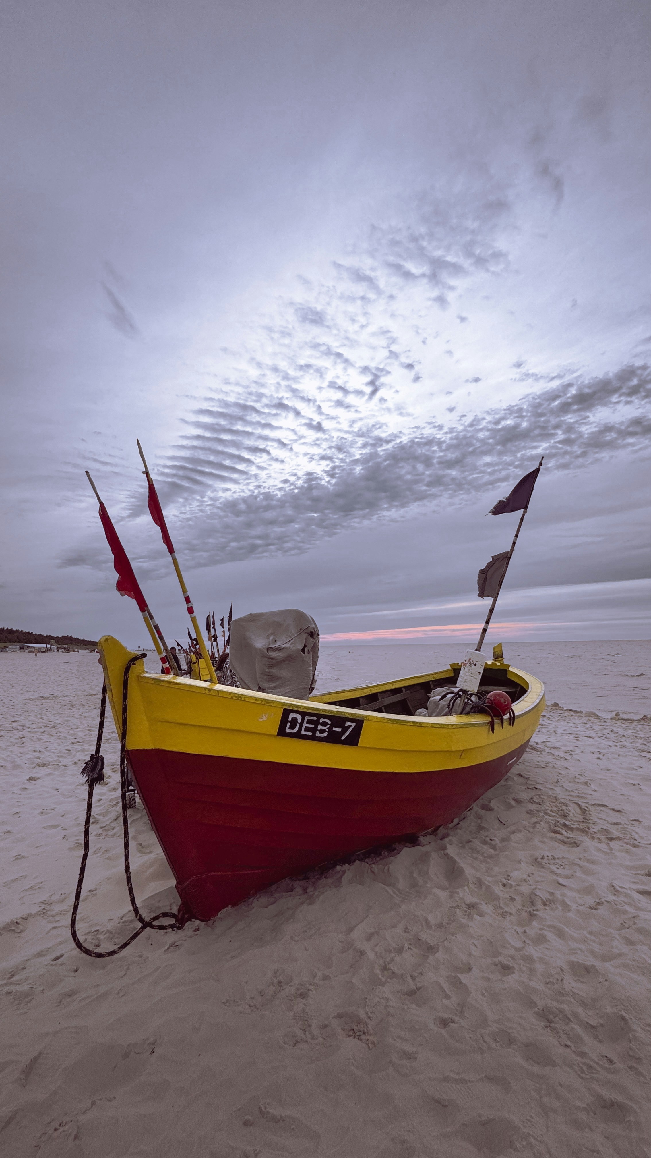 Hull on the Dune: A Vibrant Boat Beside a Quiet Beach Under Gray Skies