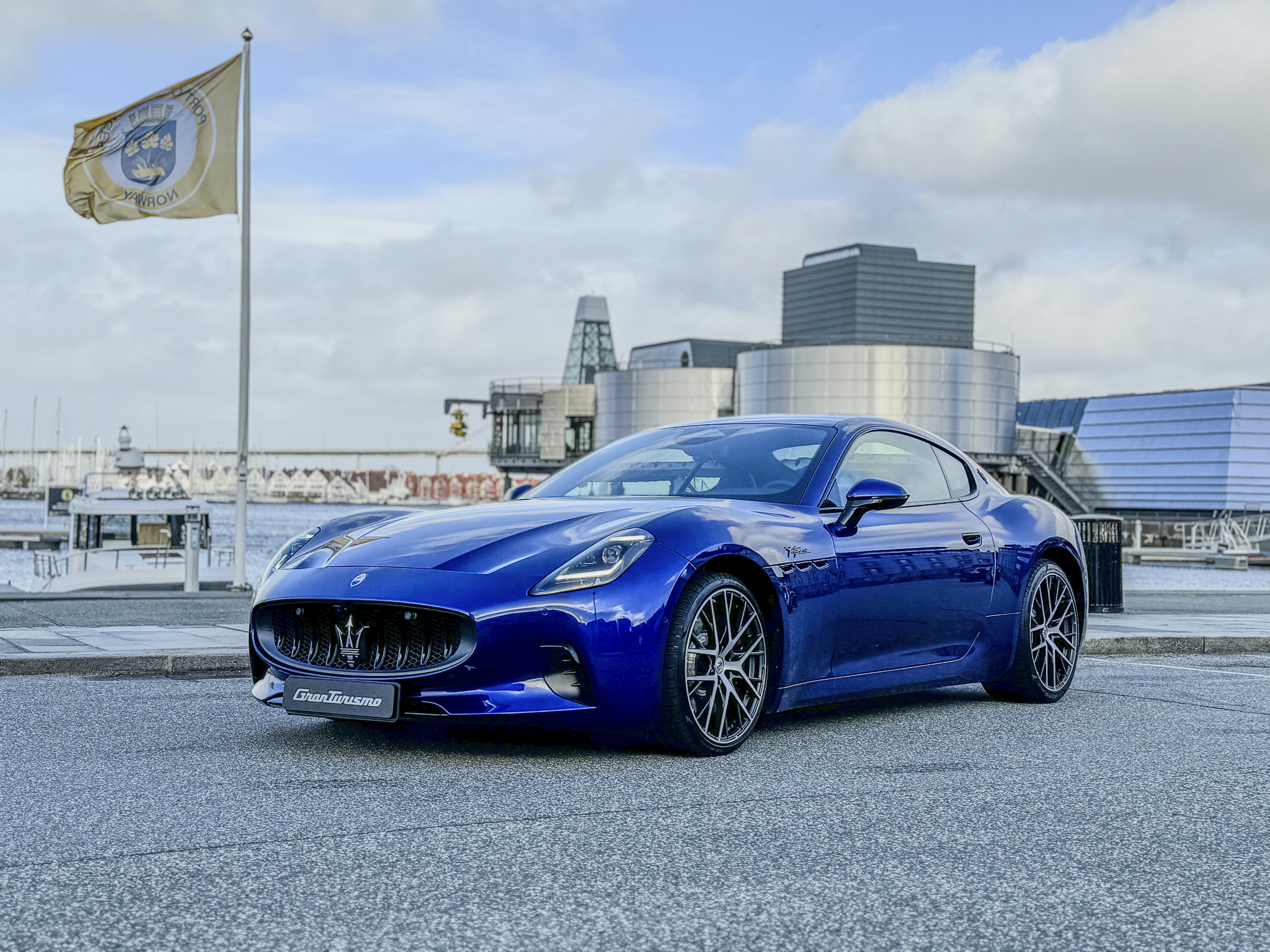 Blue sports car parked in an industrial area with modern architecture in the background.