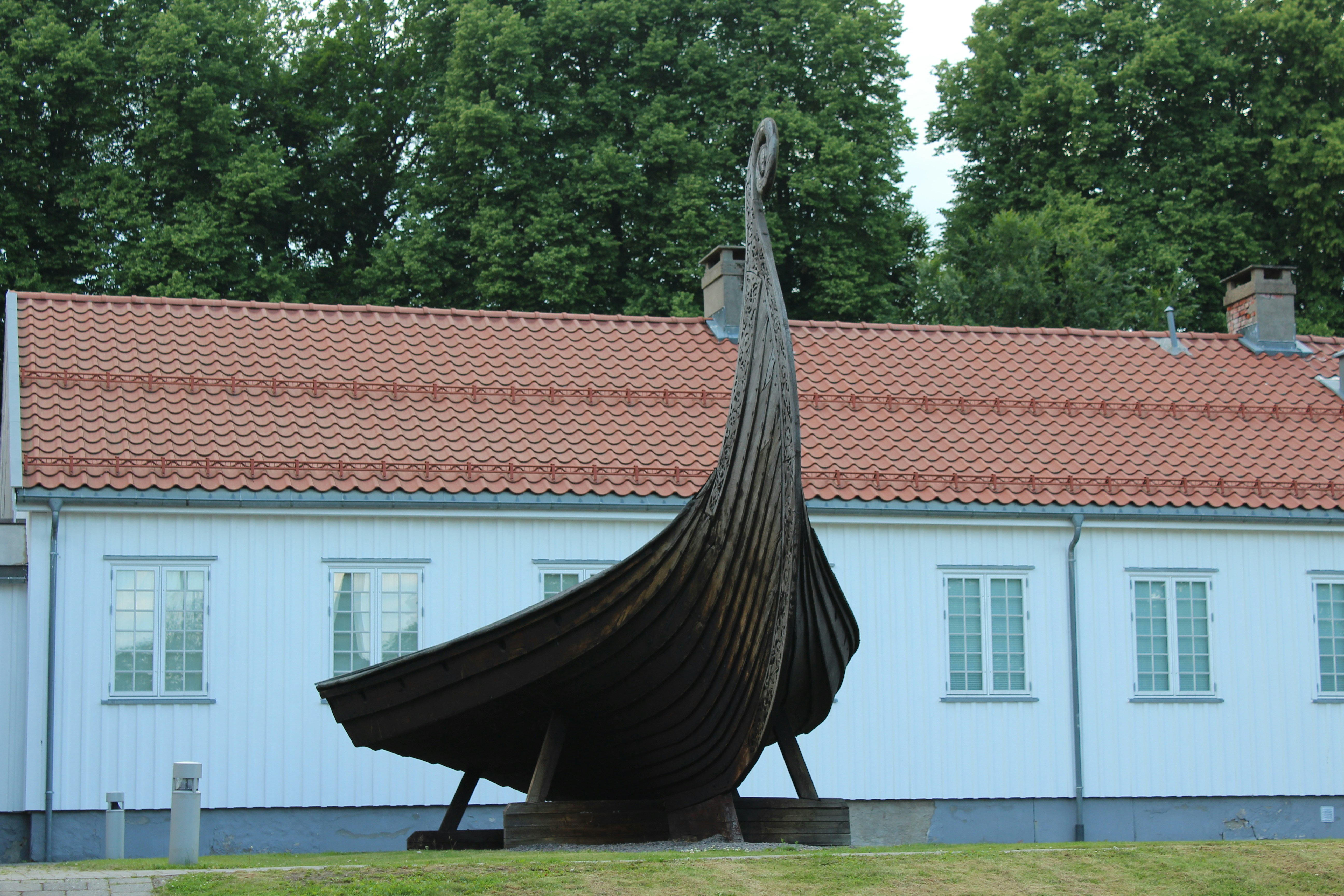 Large wooden Viking ship sculpture positioned against a backdrop of a modern building, showcasing cultural heritage. 