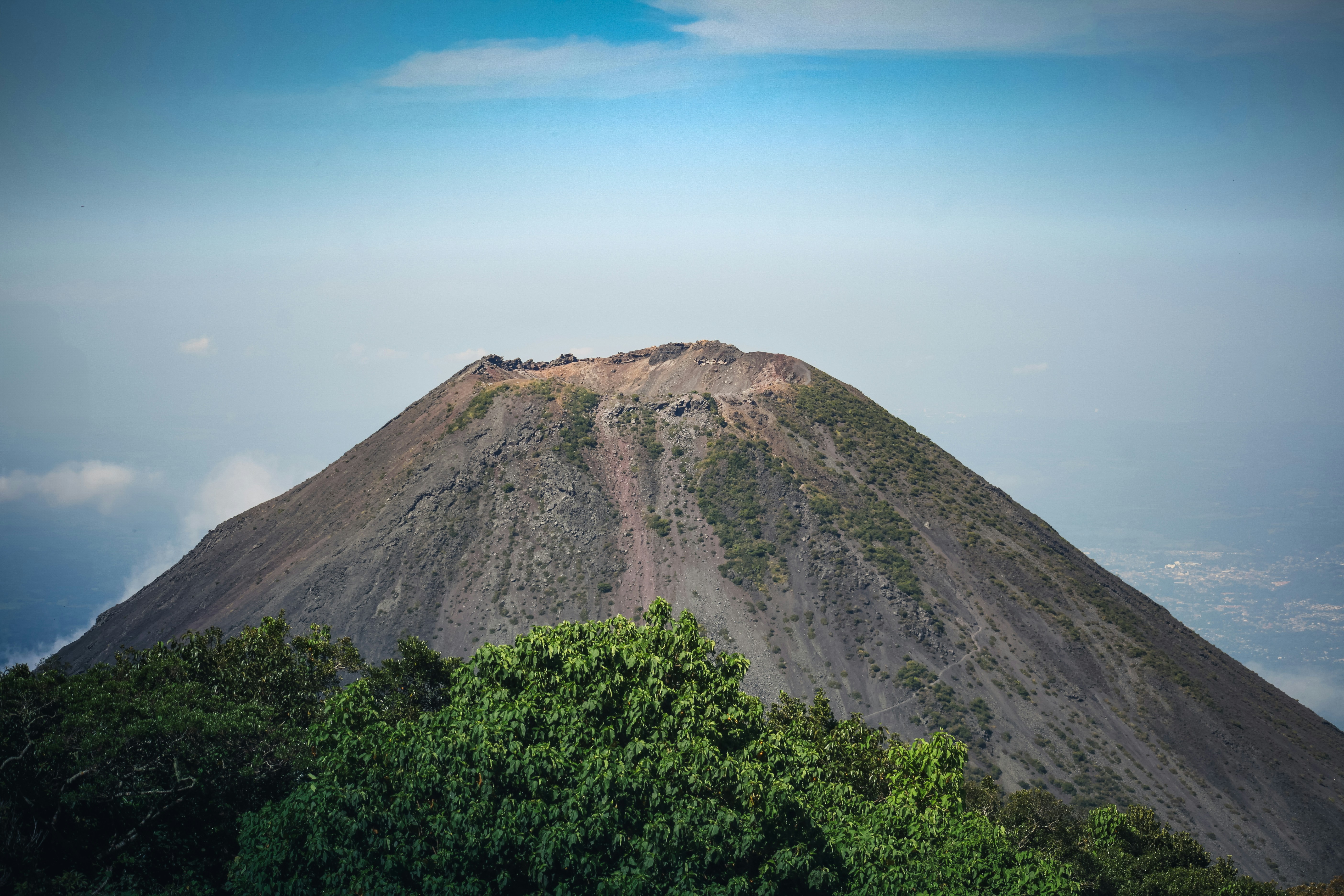Volcano summit rising above lush greenery with a clear blue sky overhead.
