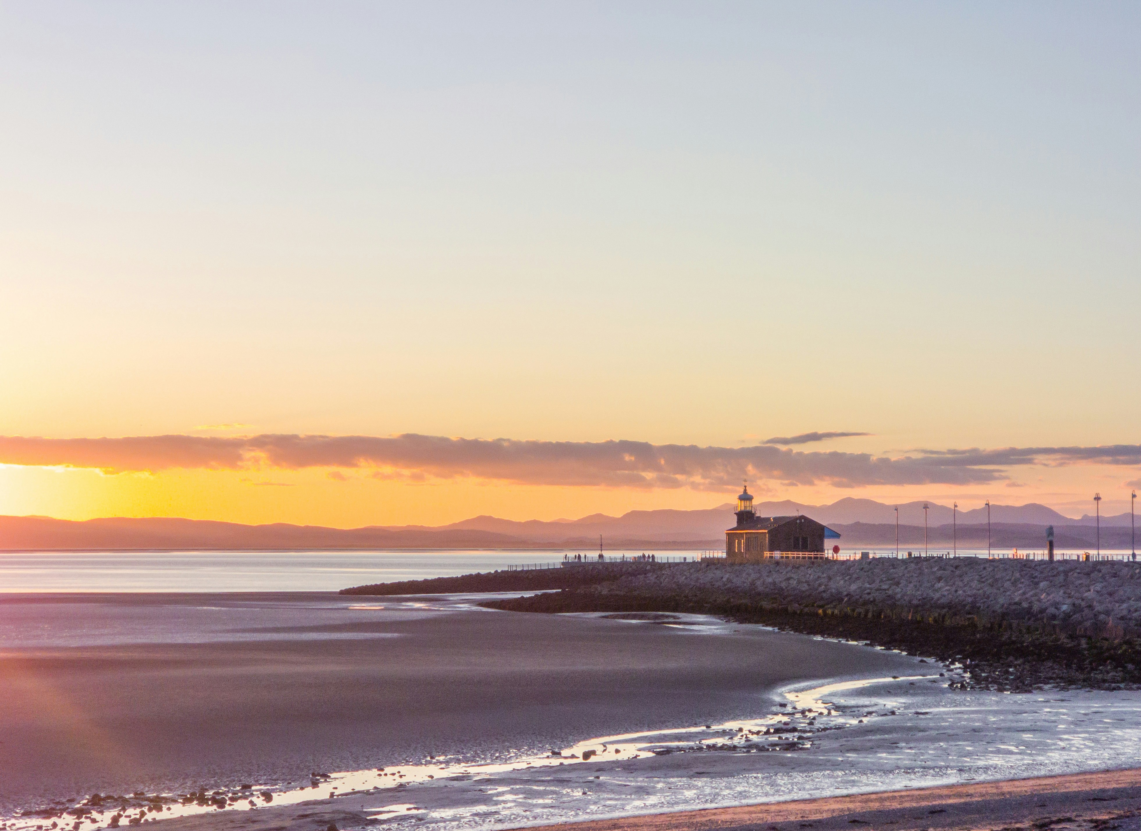 The sun is setting over a beach with a lighthouse photo – Free ...