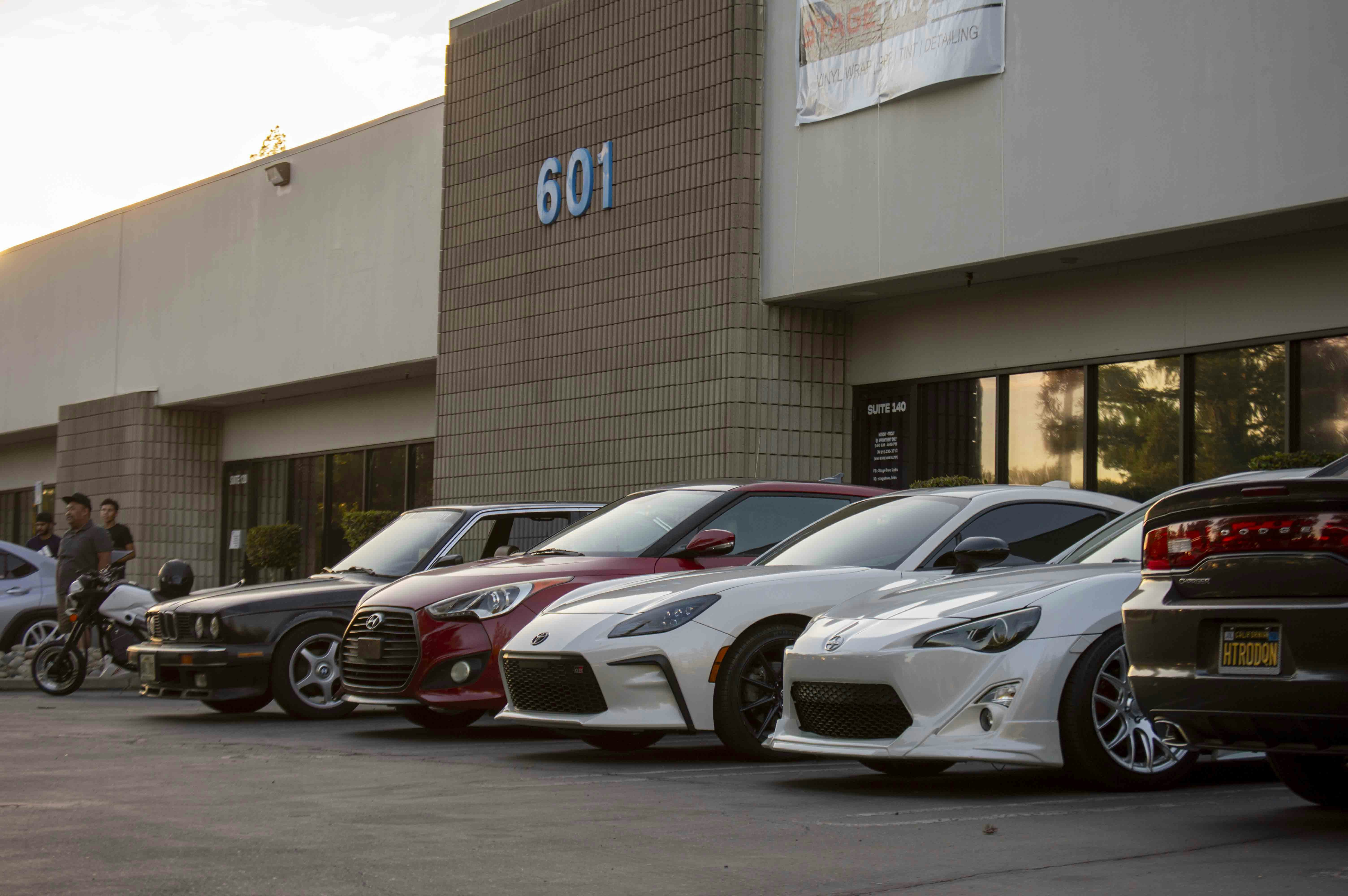 Lineup at Dusk: Sports Cars and Sedans under a Commercial Build
